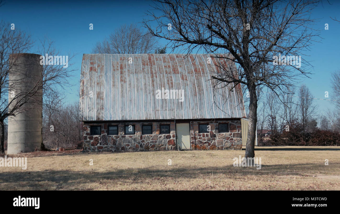 Stone barn with a rusted metal roof and silo in Southwest Missouri ...