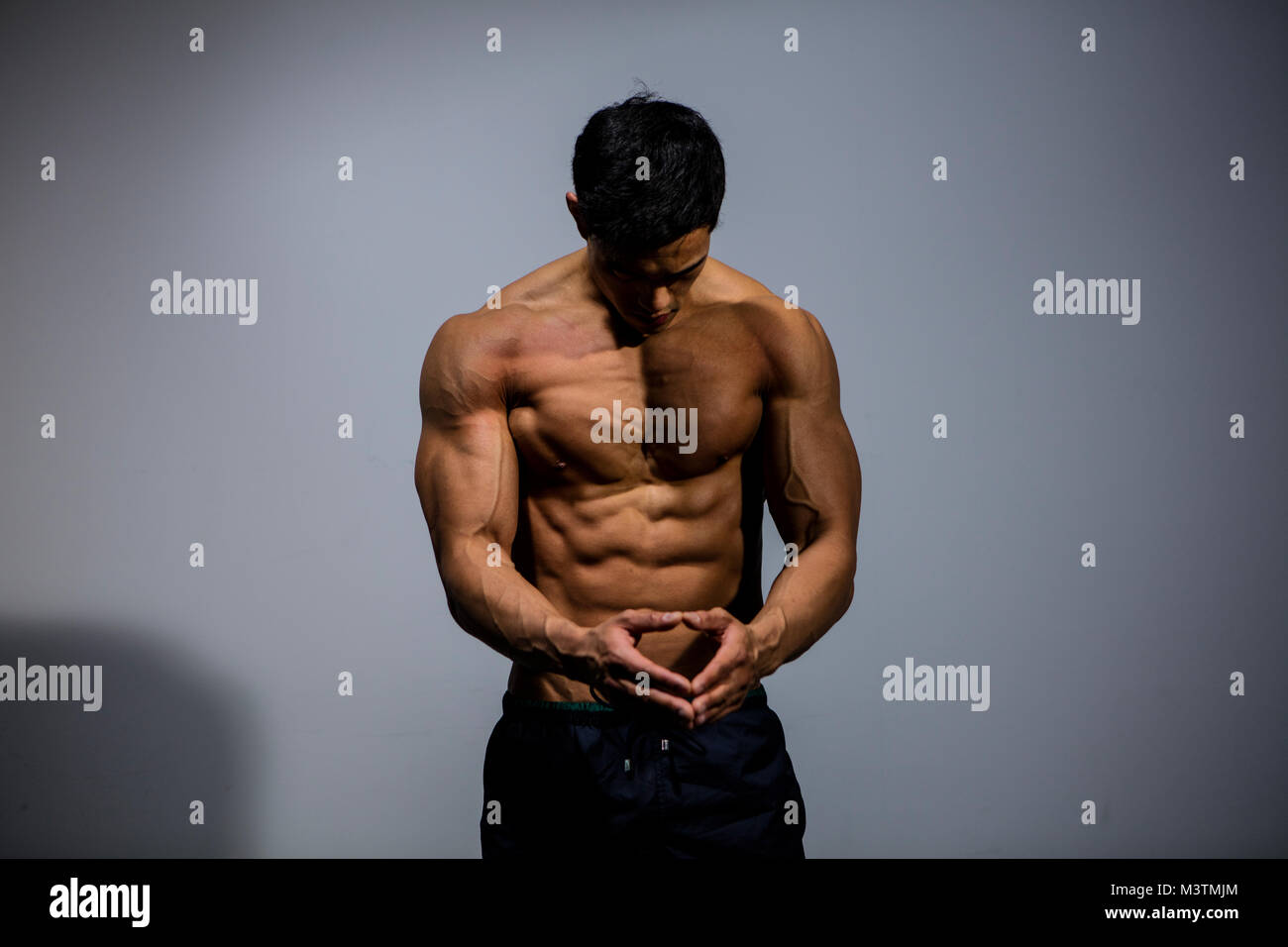 A male fitness model gathering his hands together and flexing pectoral ...