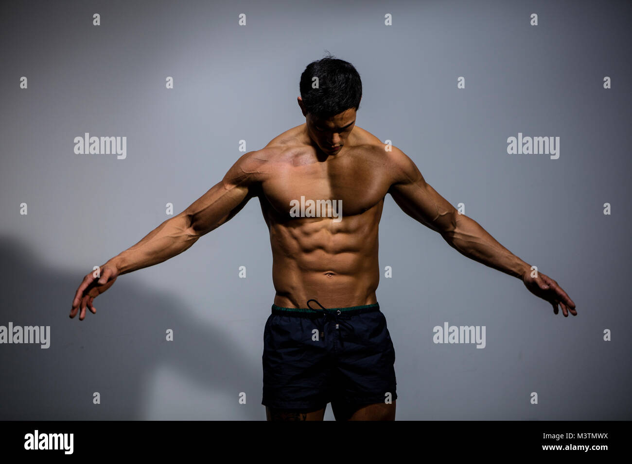 An Asian fitness model displays his biceps and pectoral muscles by ...