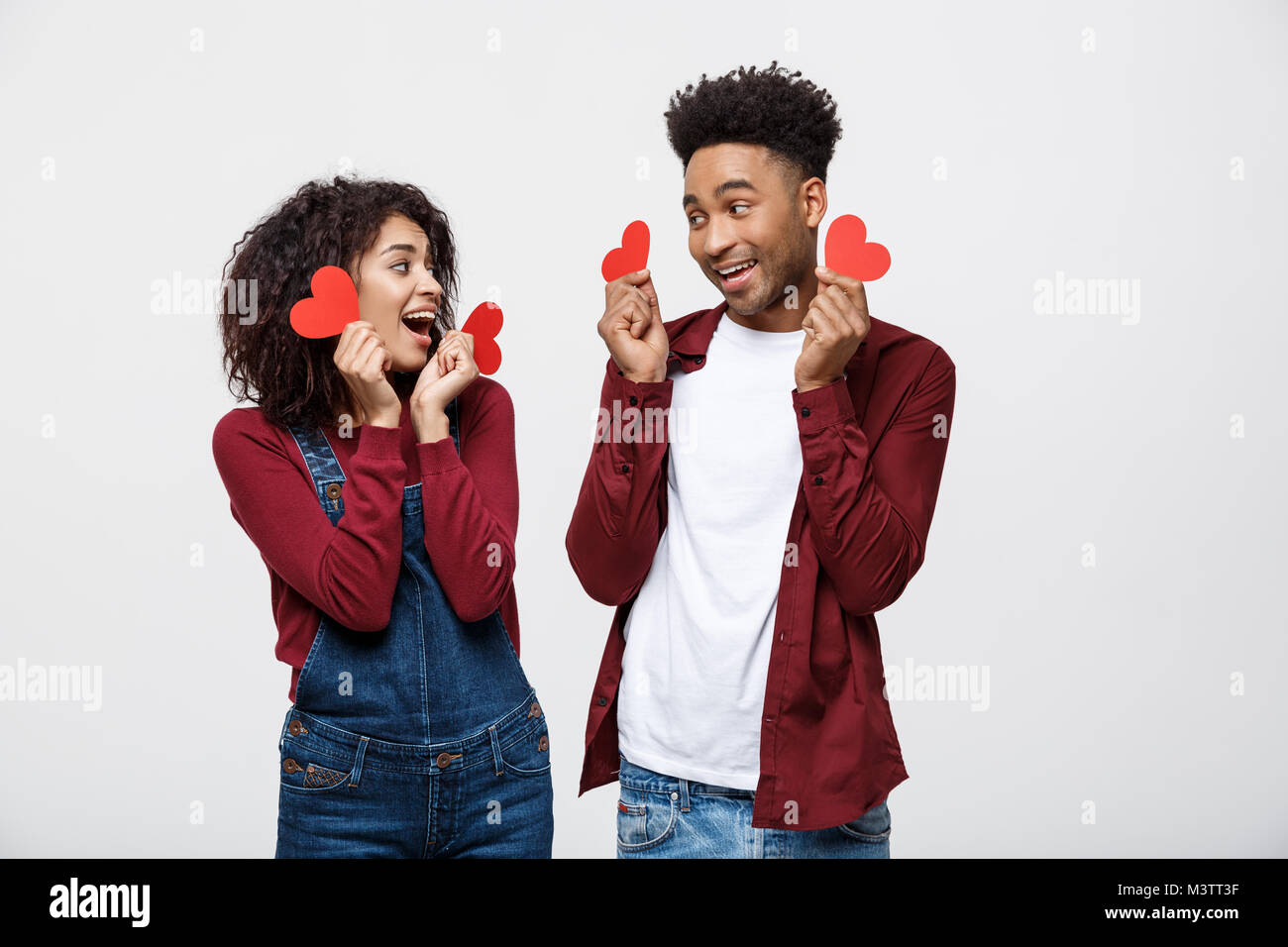 Beautiful Afro American couple holding two red paper heart, looking at ...