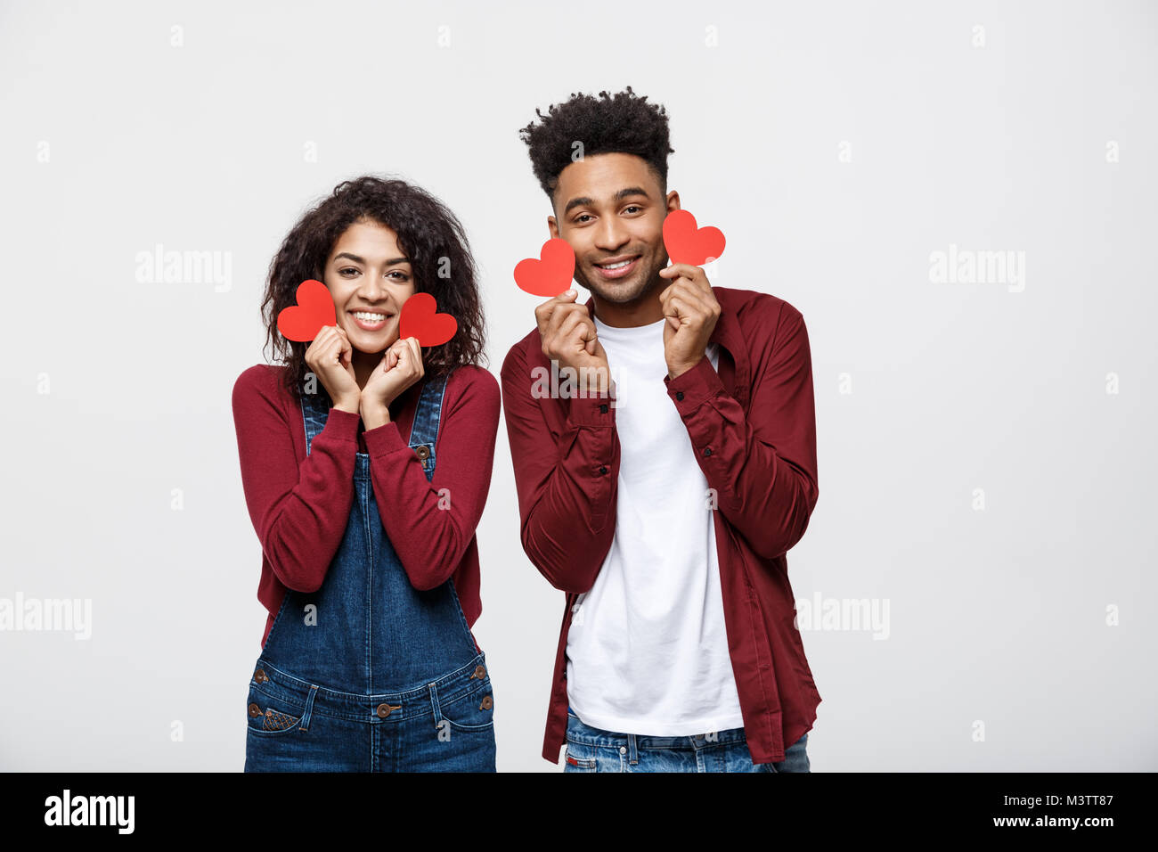 Beautiful Afro American couple holding two red paper heart, looking at ...