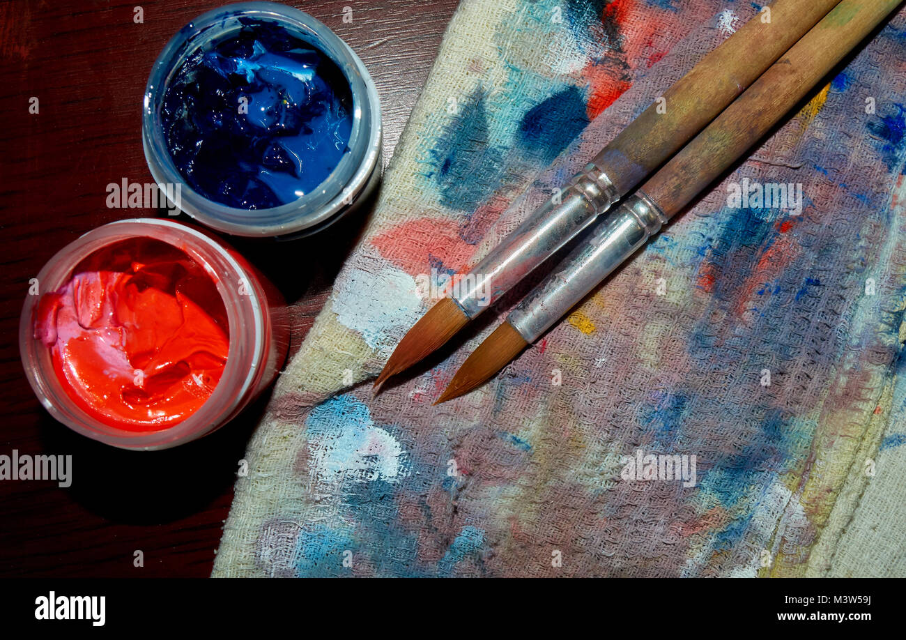 Two brushes on the colorful rag with red and dark blue gouache cans on ...