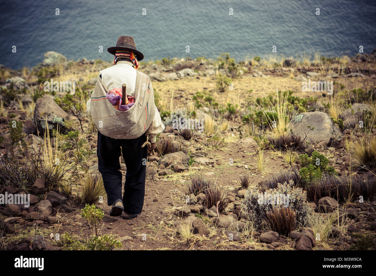 Poor man seen from behind walking down a cliff, Taquile Island ...
