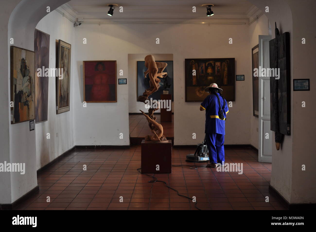 A Latin American cleaner dressed in blue cleaning the floor of an art ...