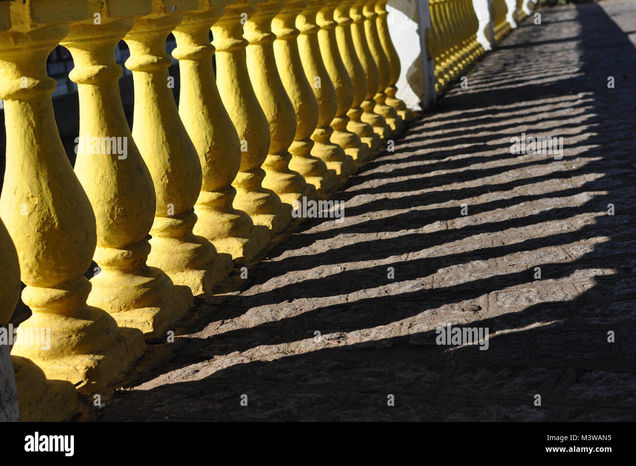 Yellow concrete posts casting shadows on a bridge in bright sunshine ...