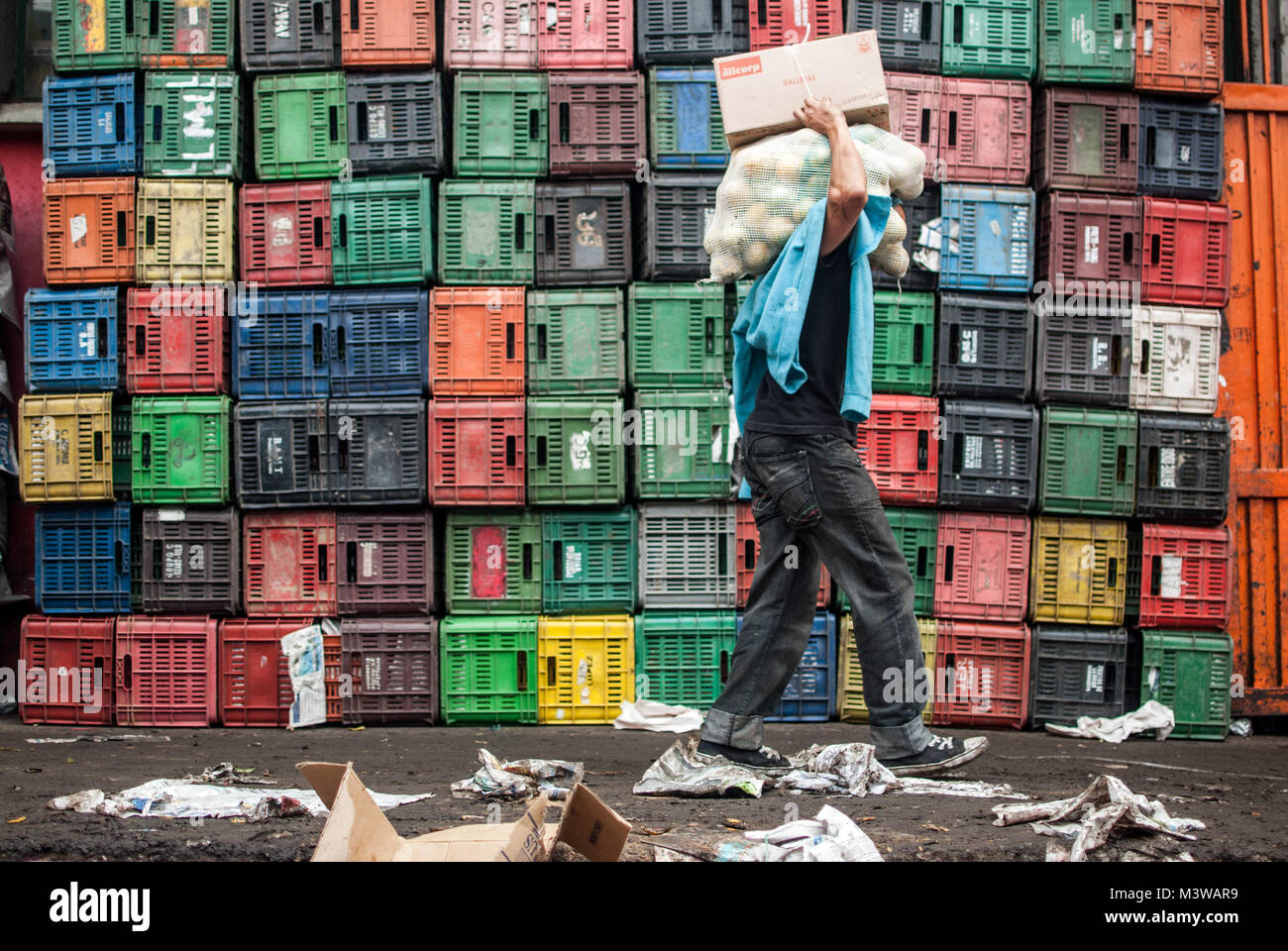 A man carrying a box and a sack while walking past a pile of plastic ...