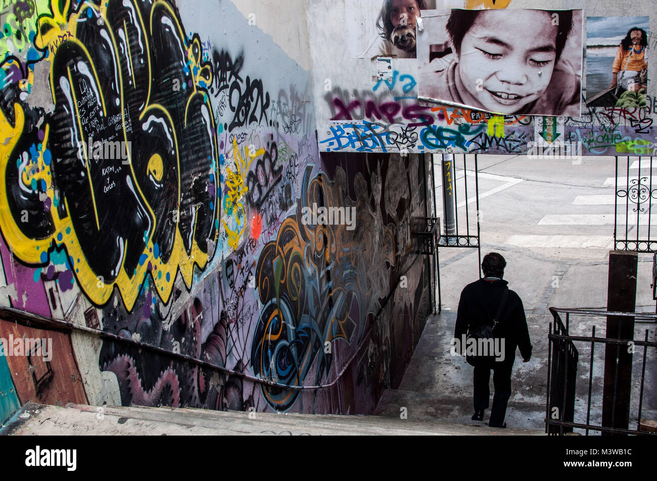 A man walking down stairs through an alleyway covered in graffiti and ...