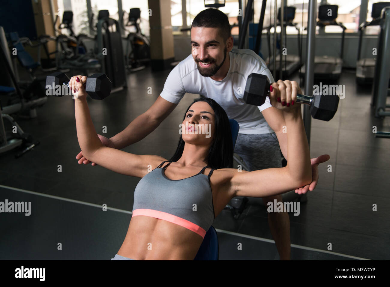 Personal Trainer Showing Young Woman How To Train Chest With Dumbbells ...