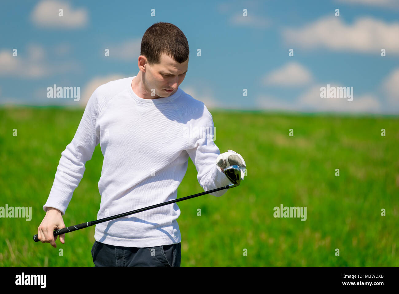portrait of a golfer inspecting his golf club before playing on the ...