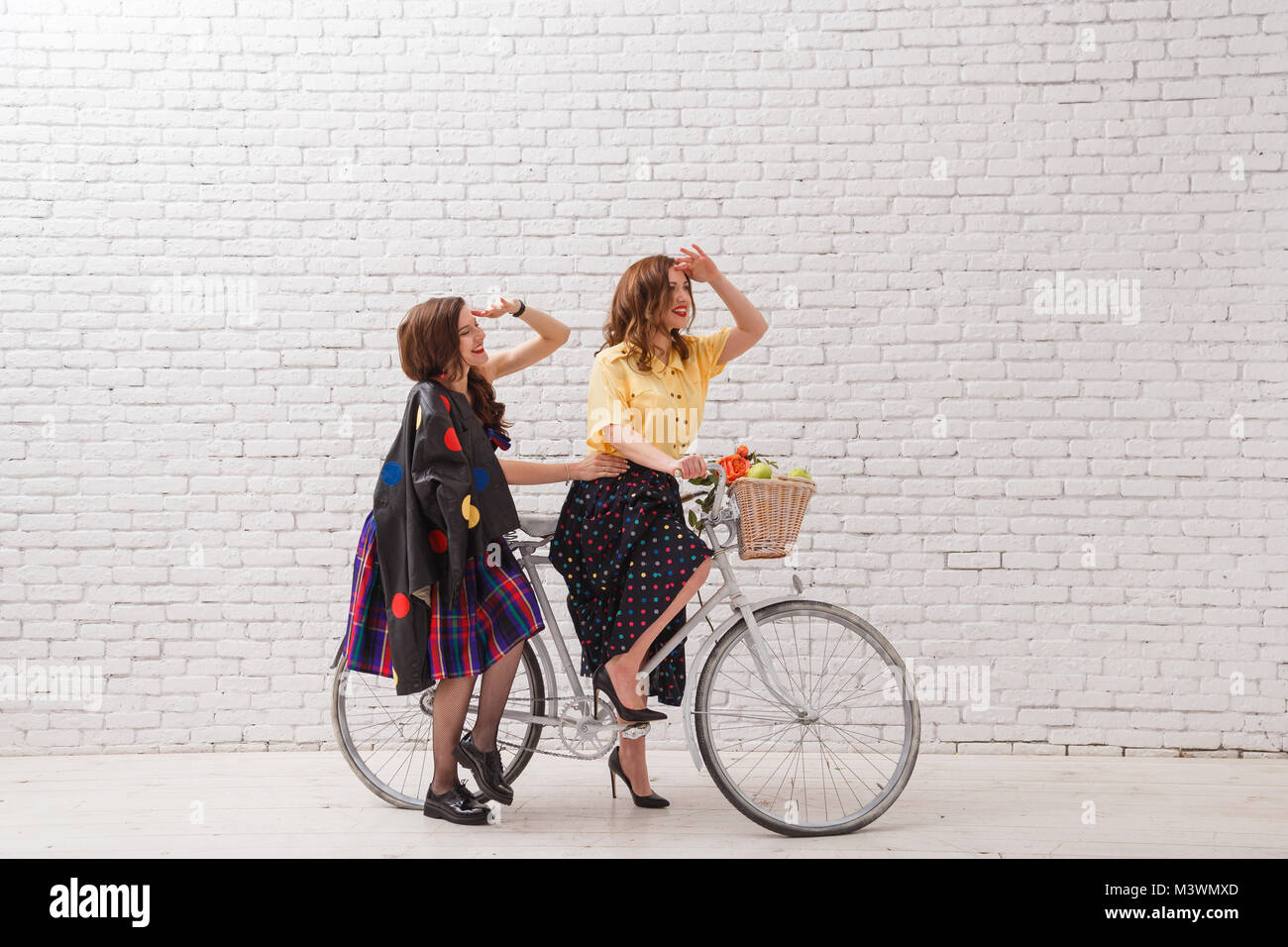 Two happy women in summer dresses are riding together on a retro bike ...