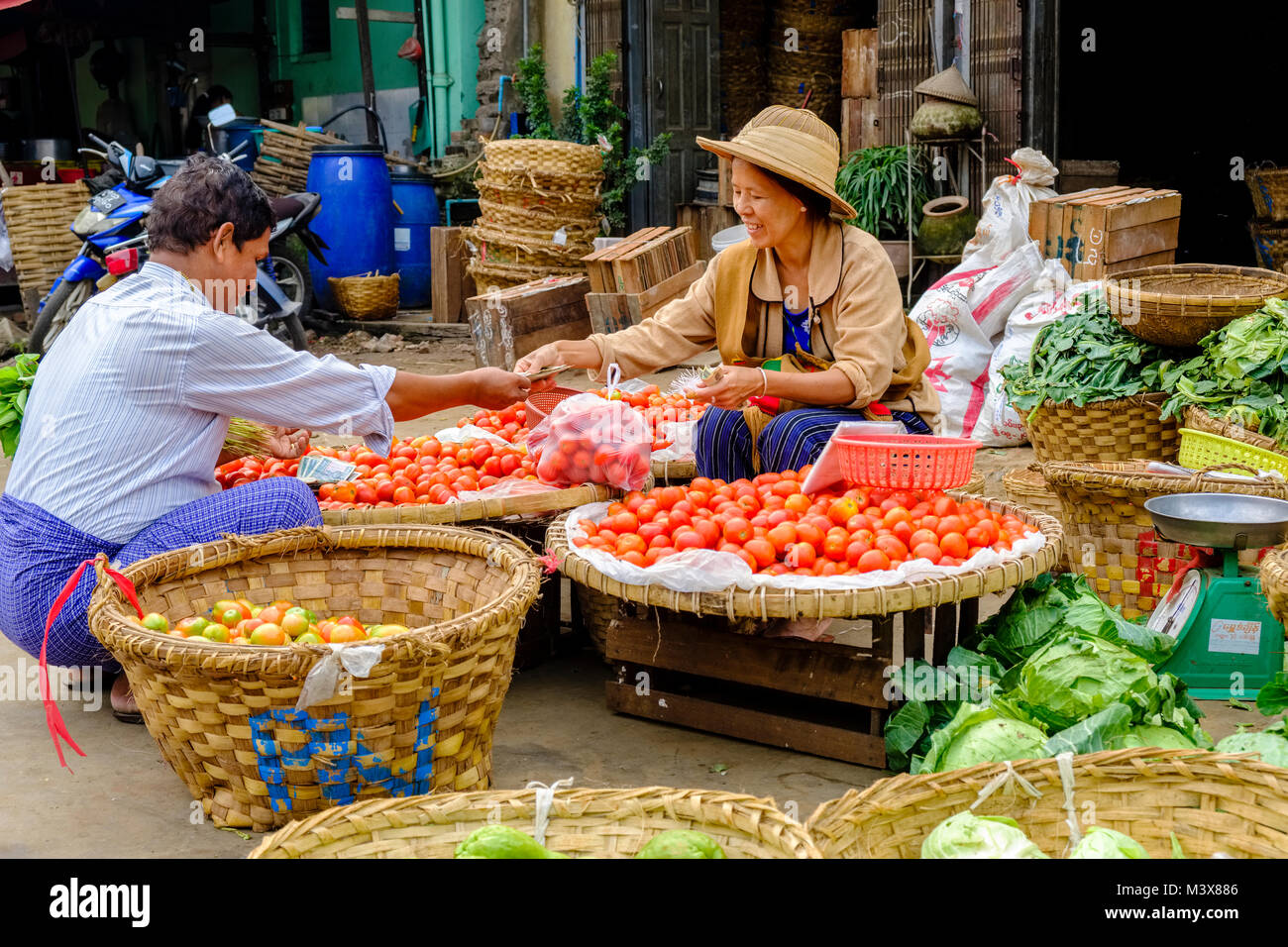 A woman is selling tomatoes and cabbage at the vegetable market in the ...