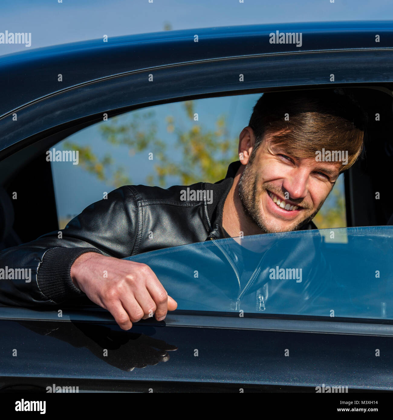 cute young man smiling and looking out of an open car window. Portrait ...