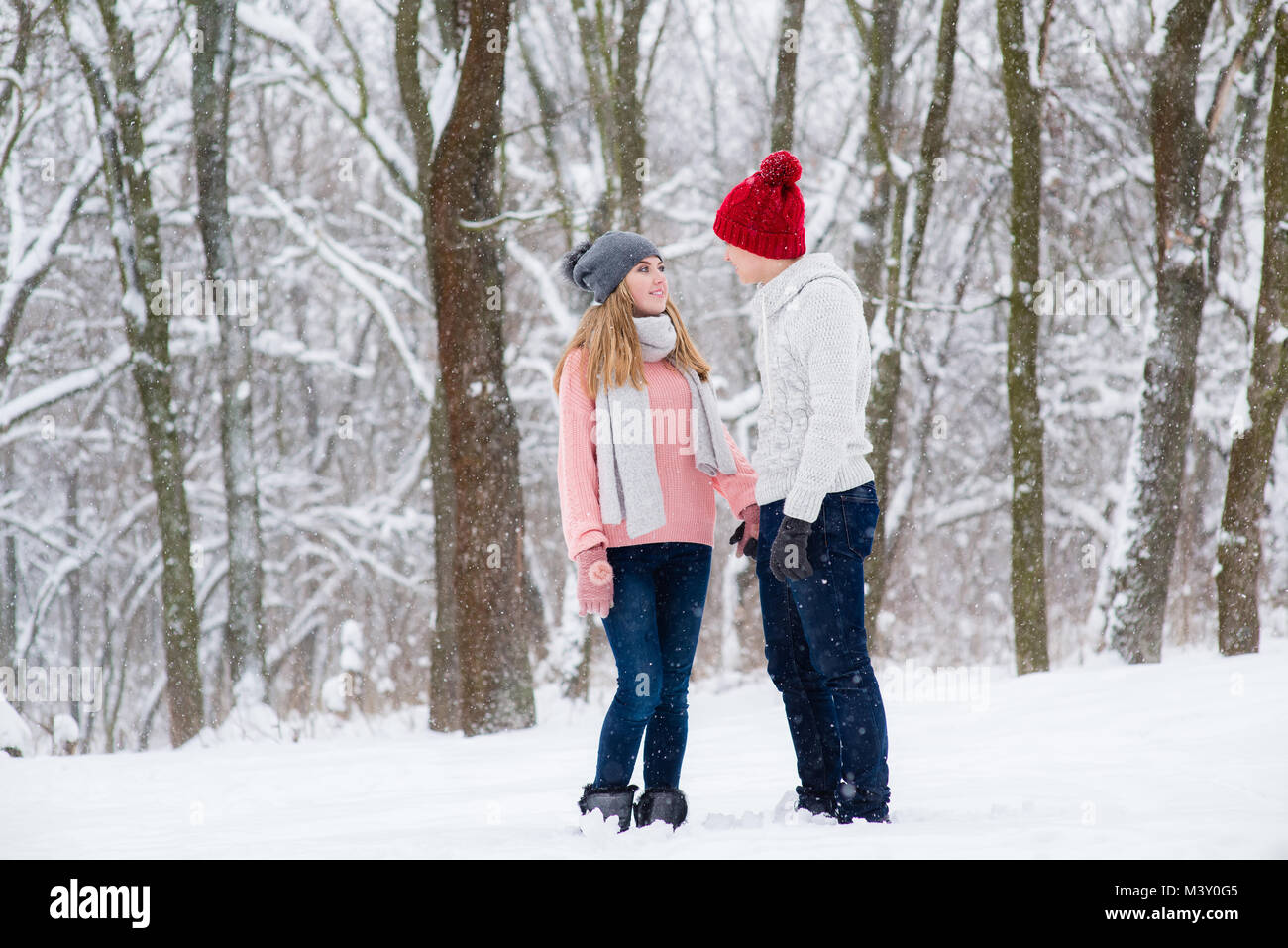 Boy and girl in warm sweaters and jeans hug and kiss at winter snow ...