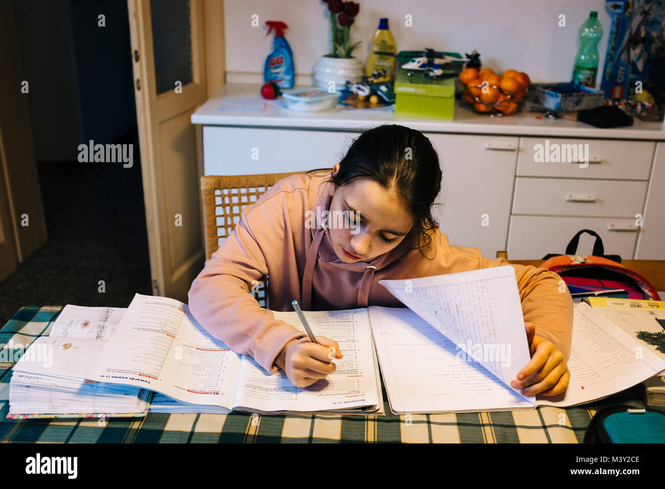 teenager performs school homework in the home kitchen on the table ...