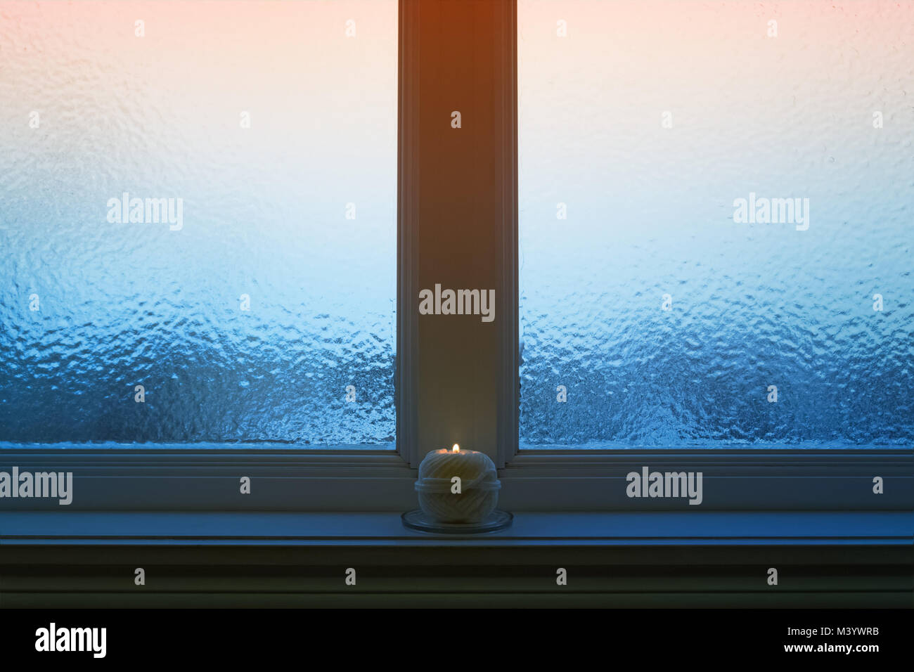 Winter evening. Frosted window, and ball of yarn decorative candle ...