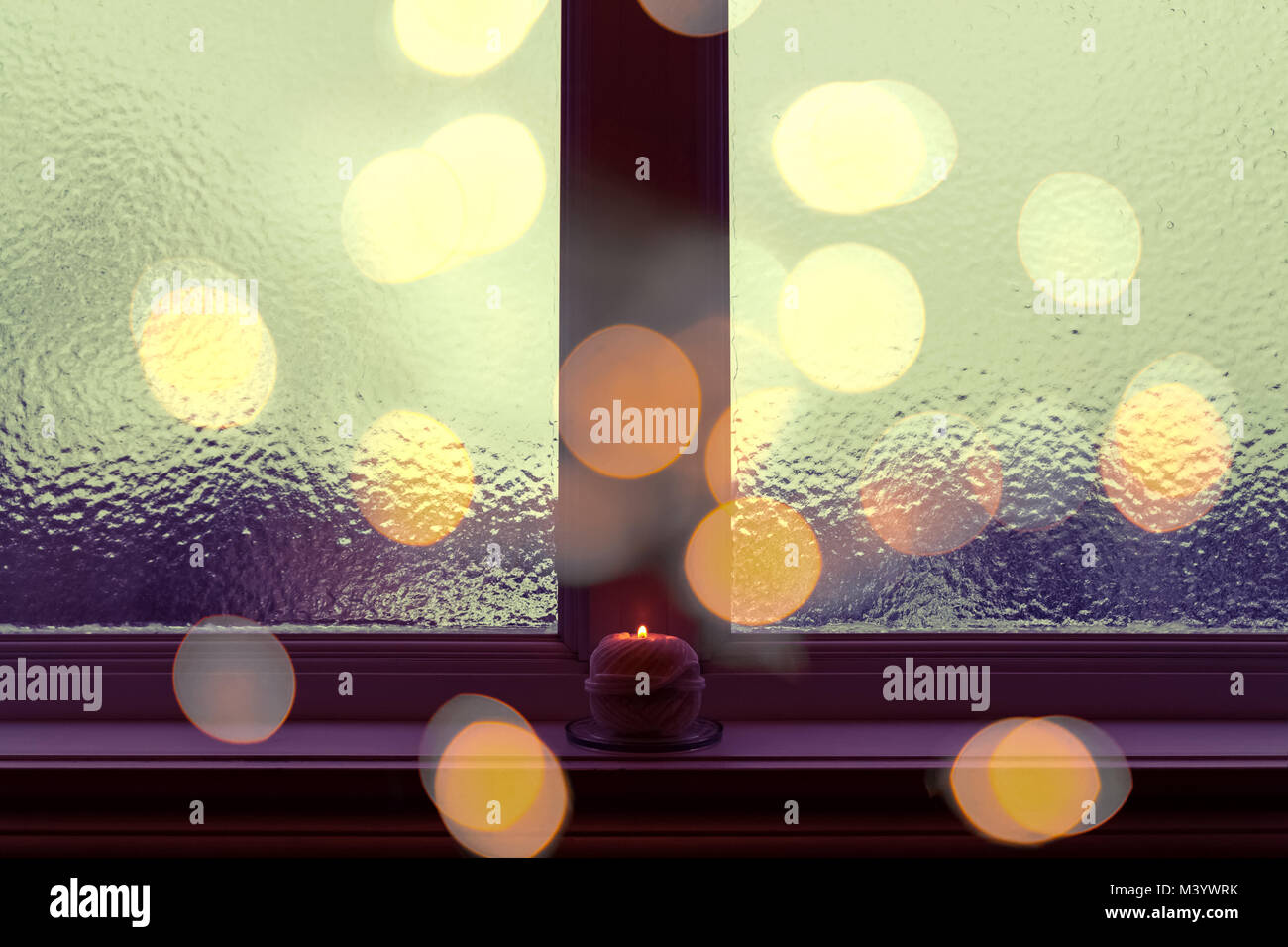 Frosted window in dark evening light, with a candle burning on a ...