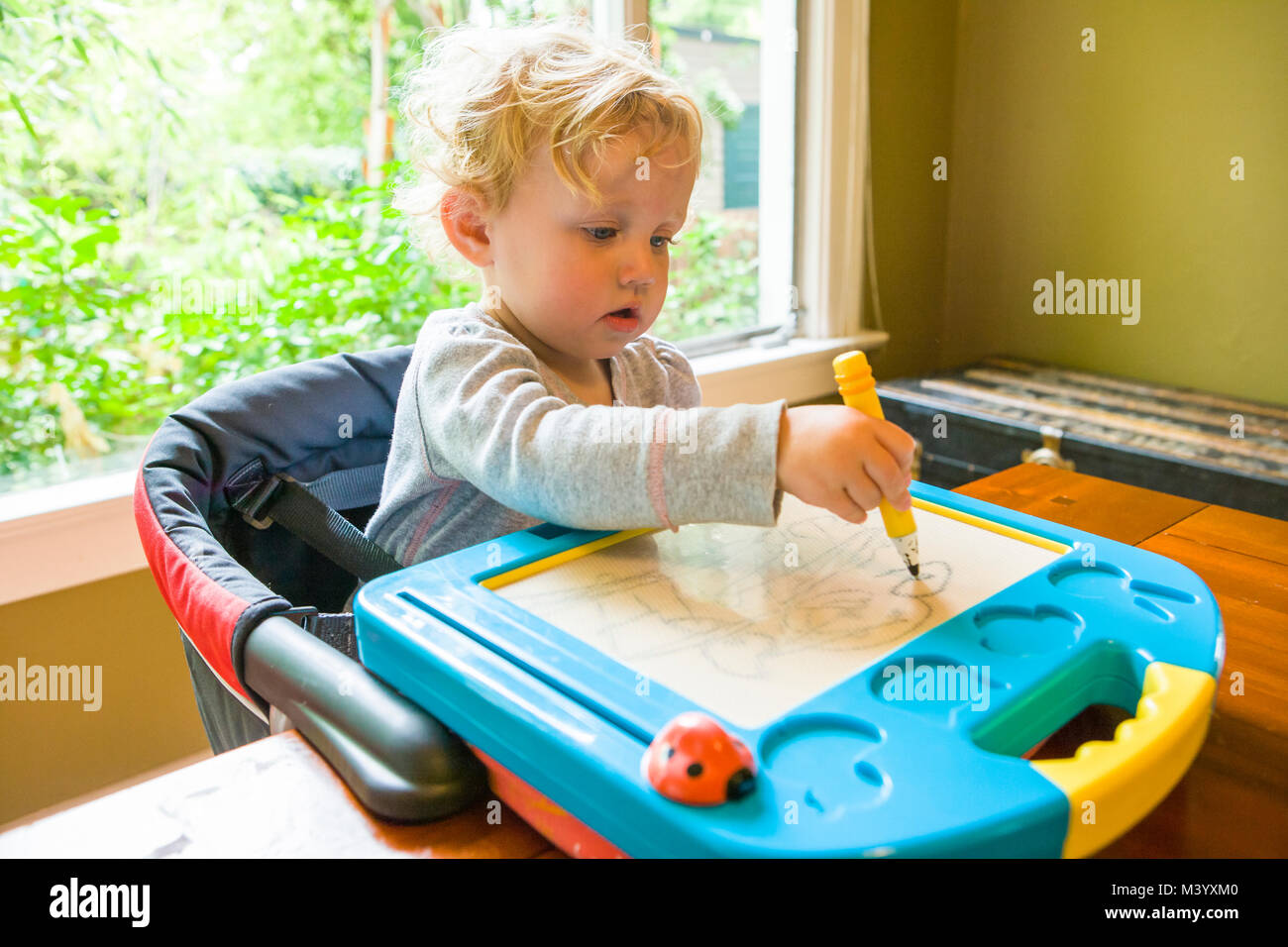 A toddler girl sitting at a table drawing with a marker Stock Photo - Alamy