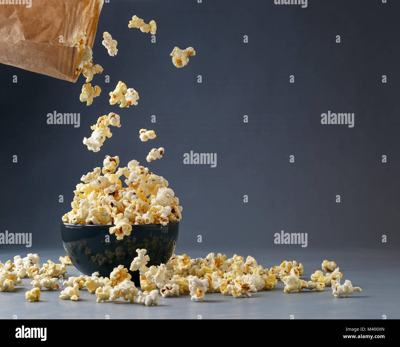 Popcorn flying into the bowl from brown paper package over grey ...