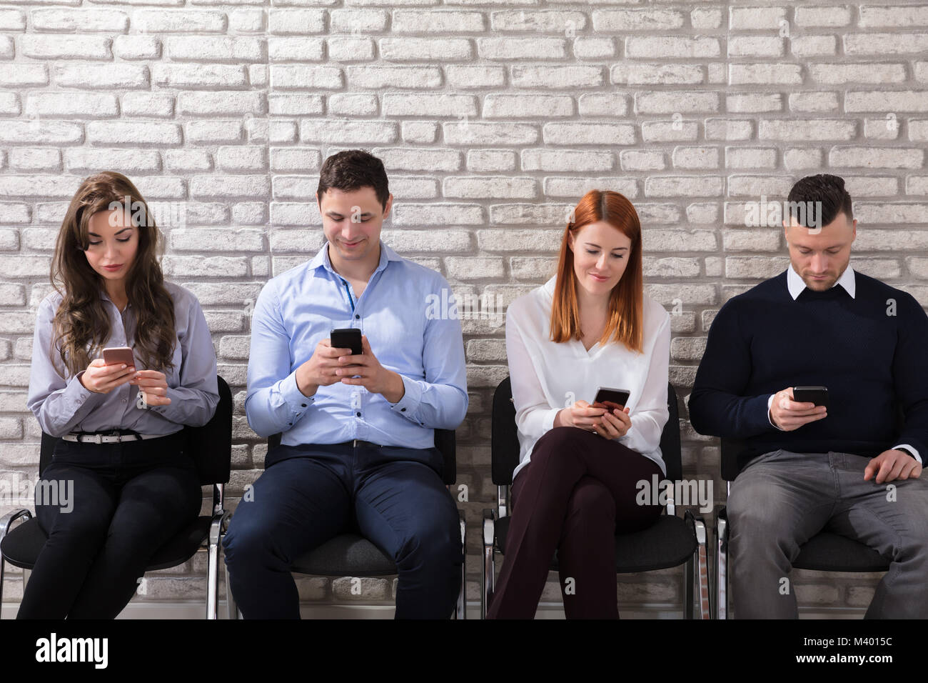 Young Business People Sitting On Chair Using Cell Phone Against Brick ...