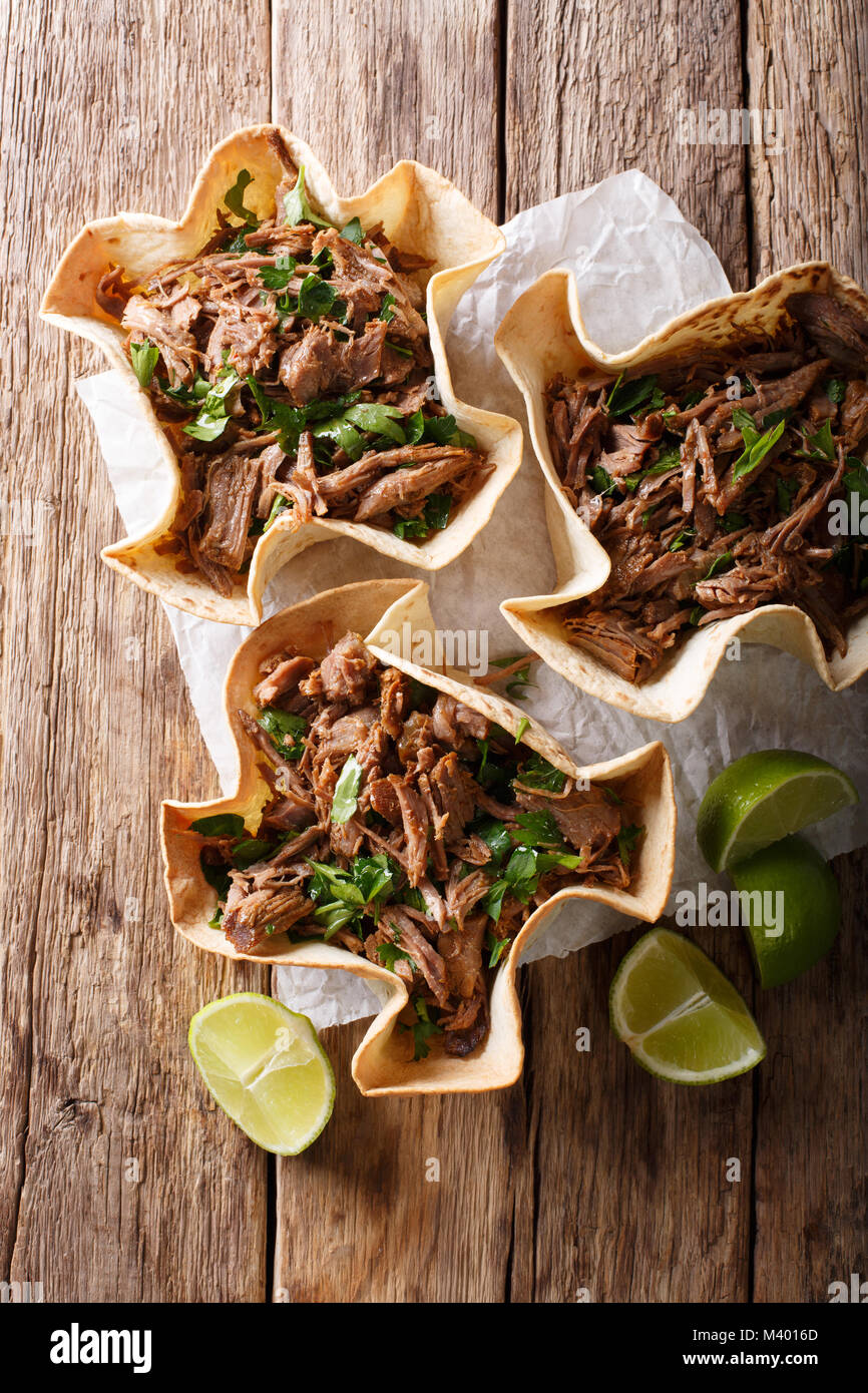 Mexican barbacoa with beef, lime and greens close-up on paper on table ...