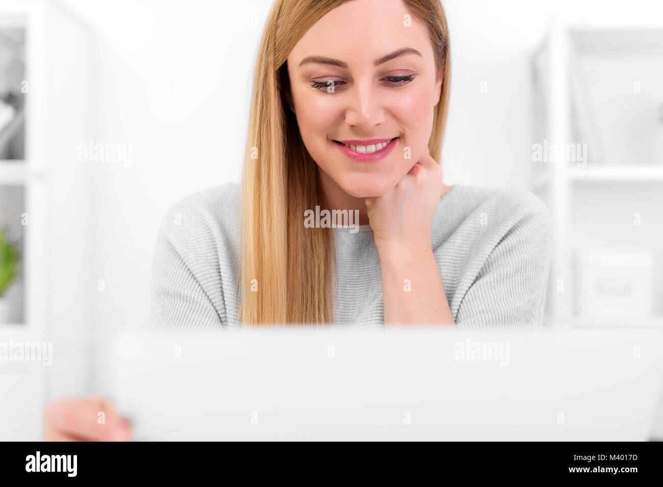 Blonde at her desk at home or in the office with a laptop and a red cup ...