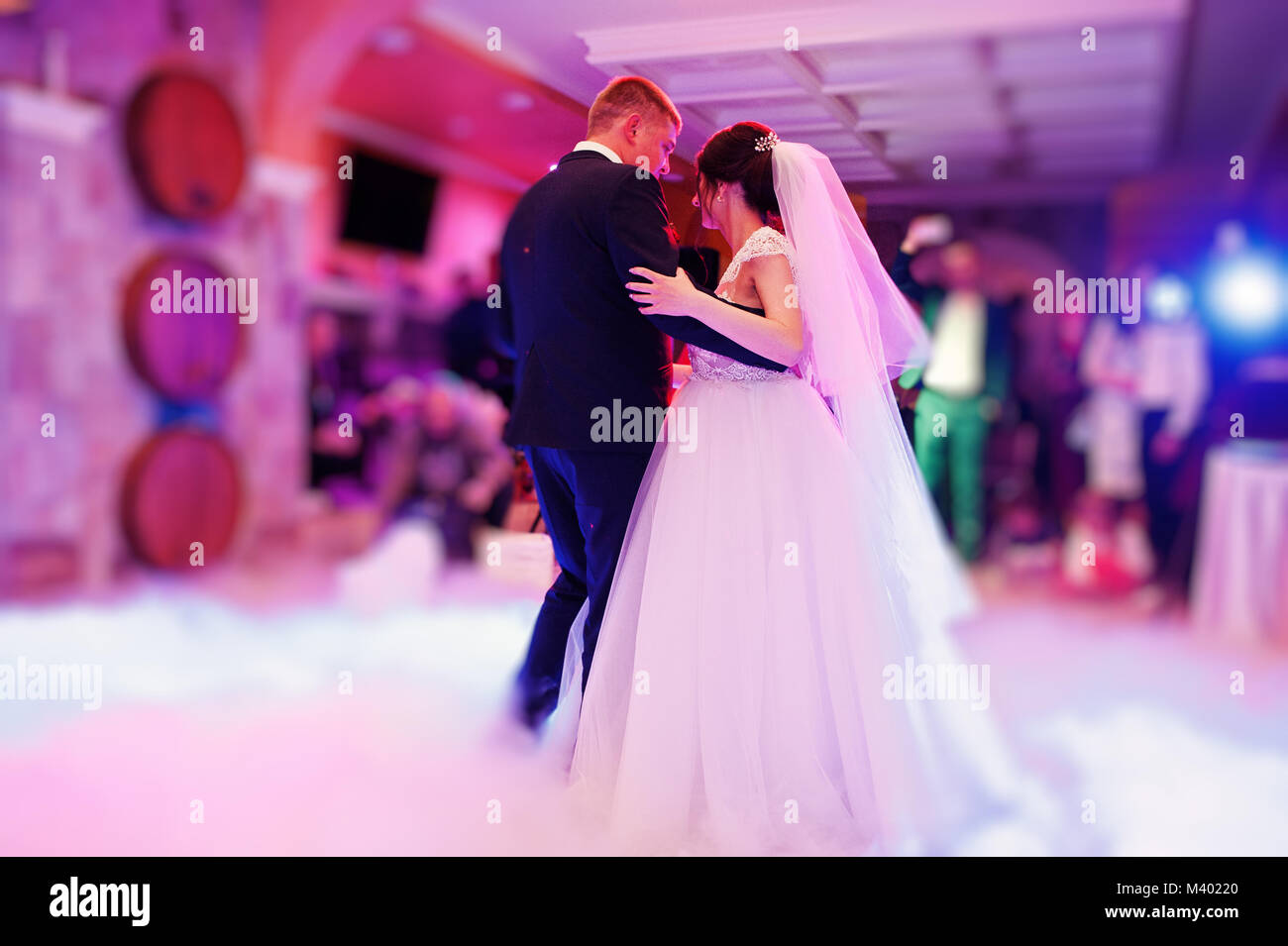 Happy young wedding couple dancing their first dance with different lights and heavy smoke in ...