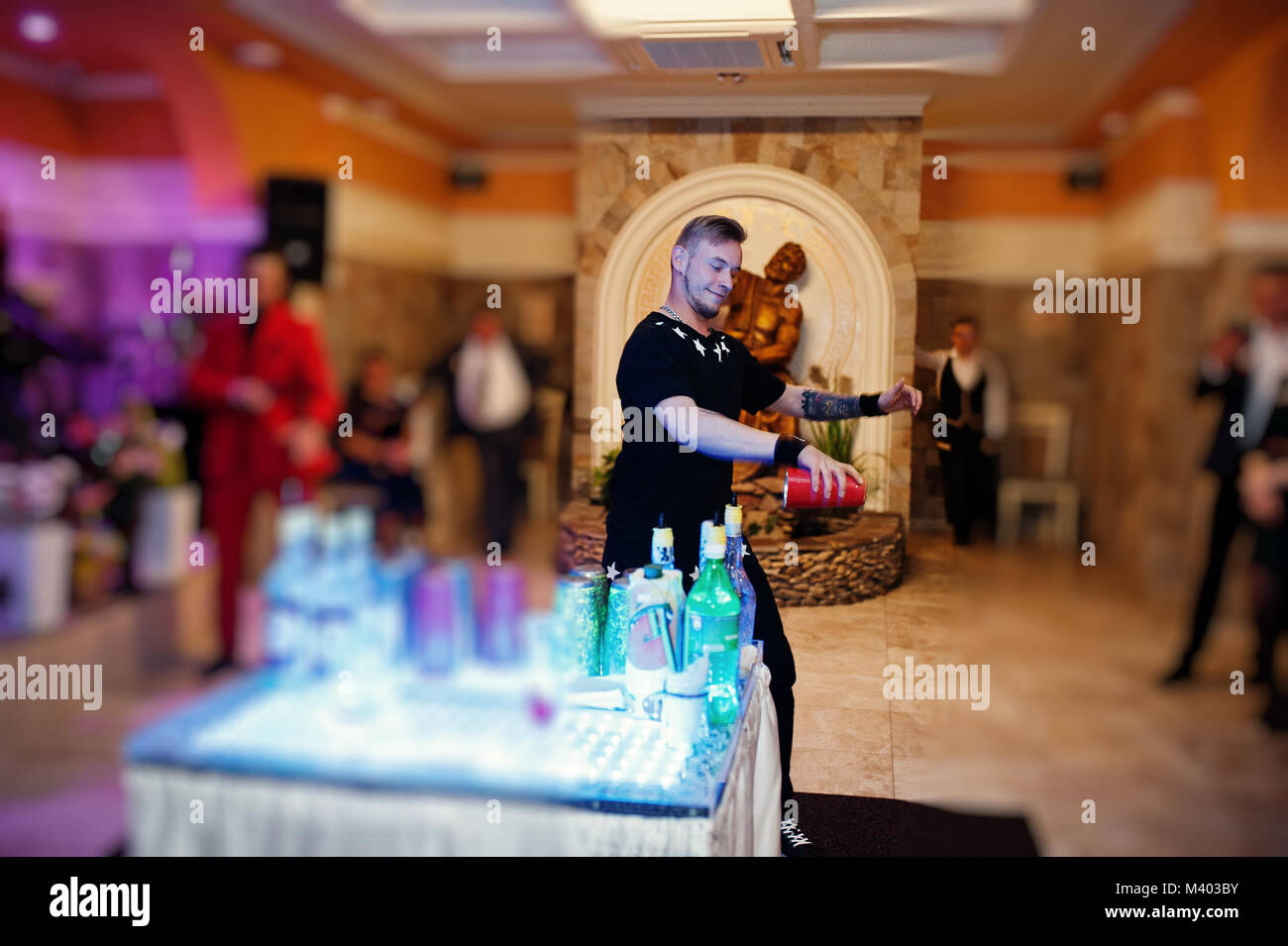 Talented bartender performing tricks with bottles and glasses in front ...