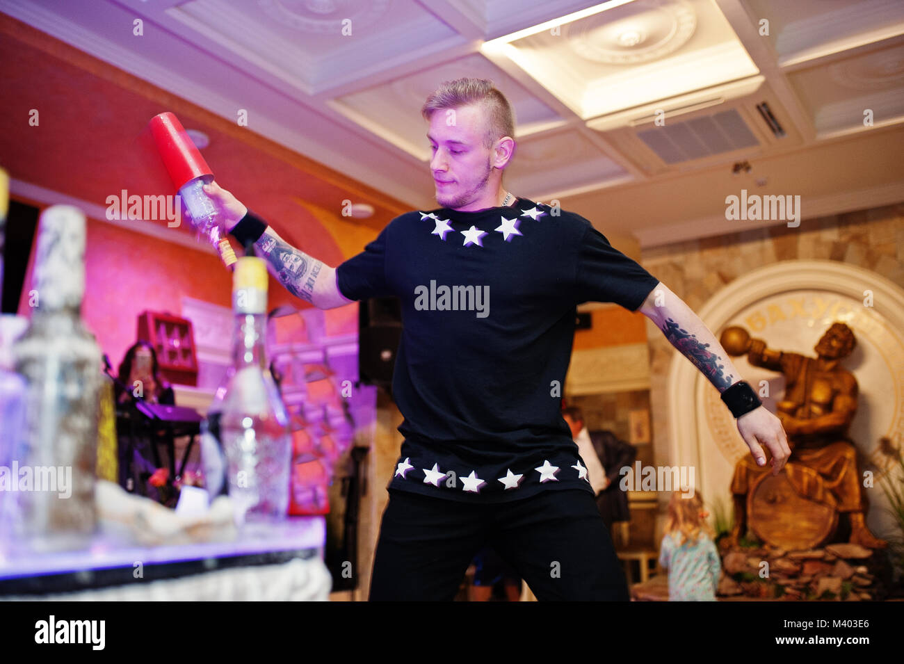 Talented bartender performing tricks with bottles and glasses in front ...