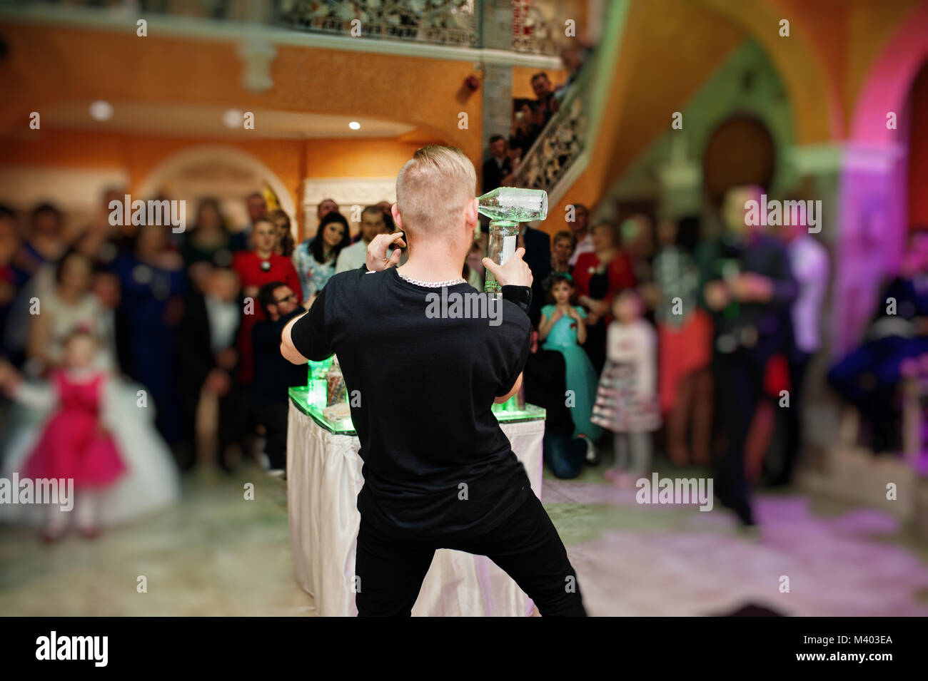 Talented bartender performing tricks with bottles and glasses in front ...