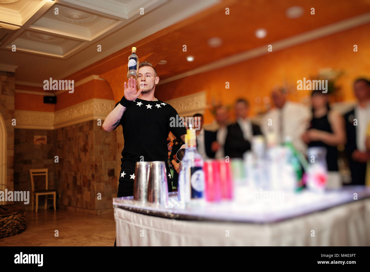 Talented bartender performing tricks with bottles and glasses in front ...