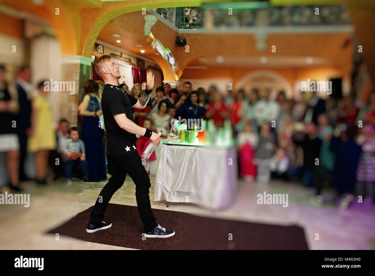 Talented bartender performing tricks with bottles and glasses in front ...