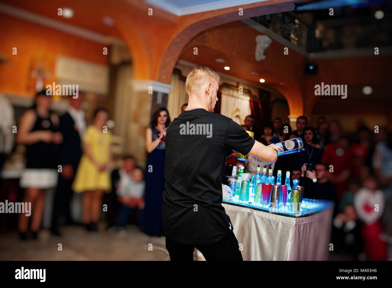 Talented bartender performing tricks with bottles and glasses in front ...