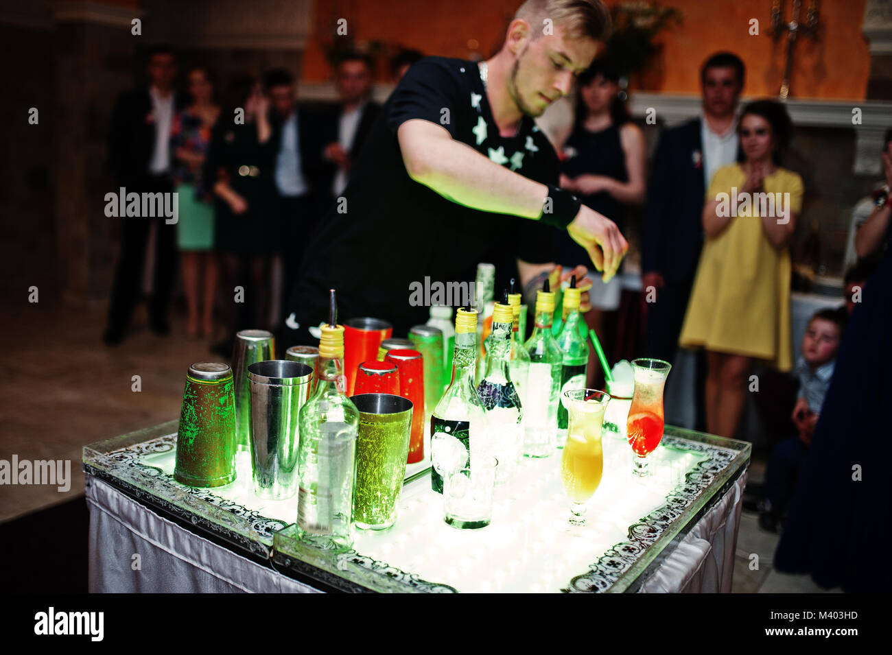 Talented bartender performing tricks with bottles and glasses in front ...