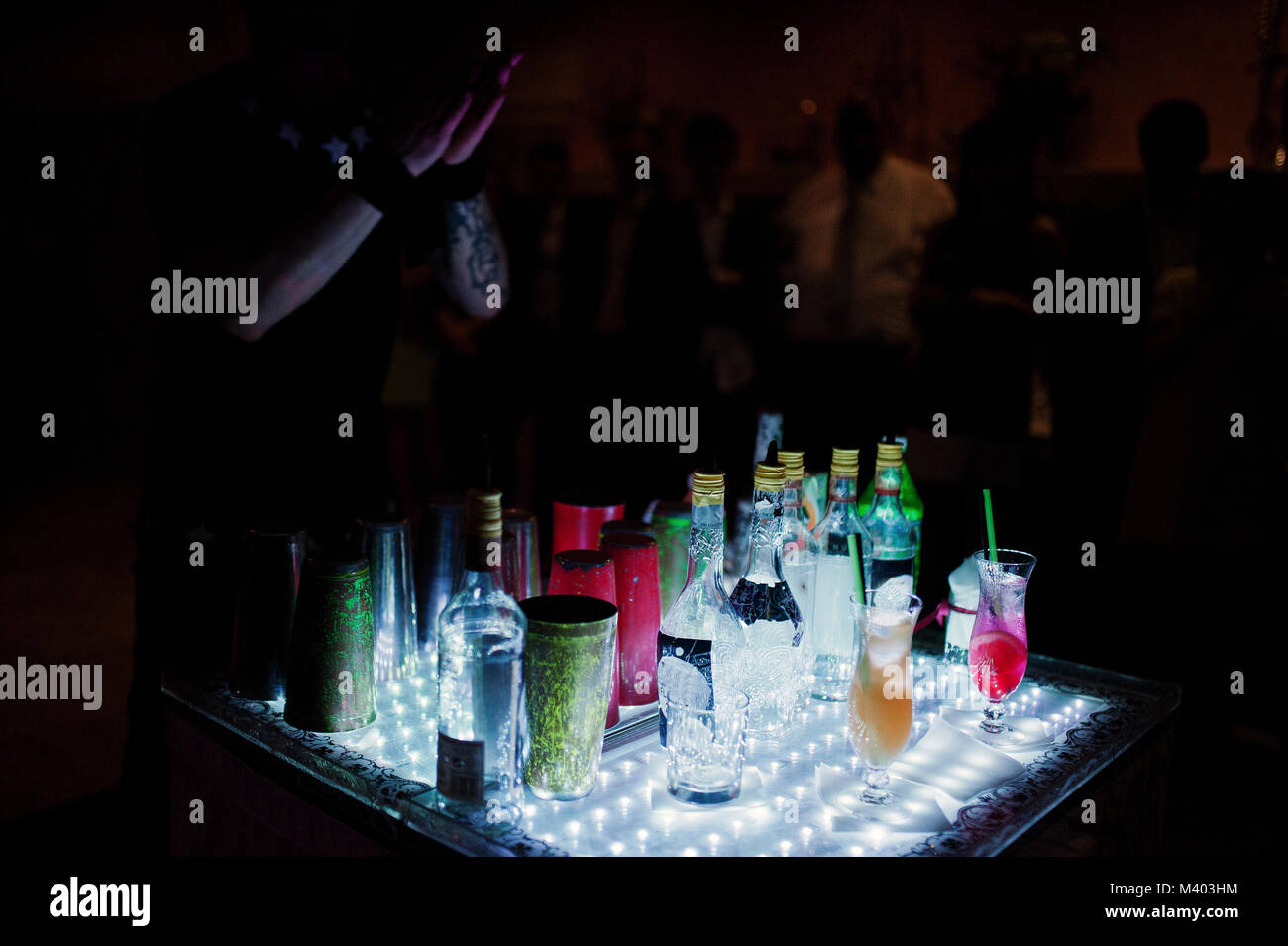 Talented bartender performing tricks with bottles and glasses in front ...