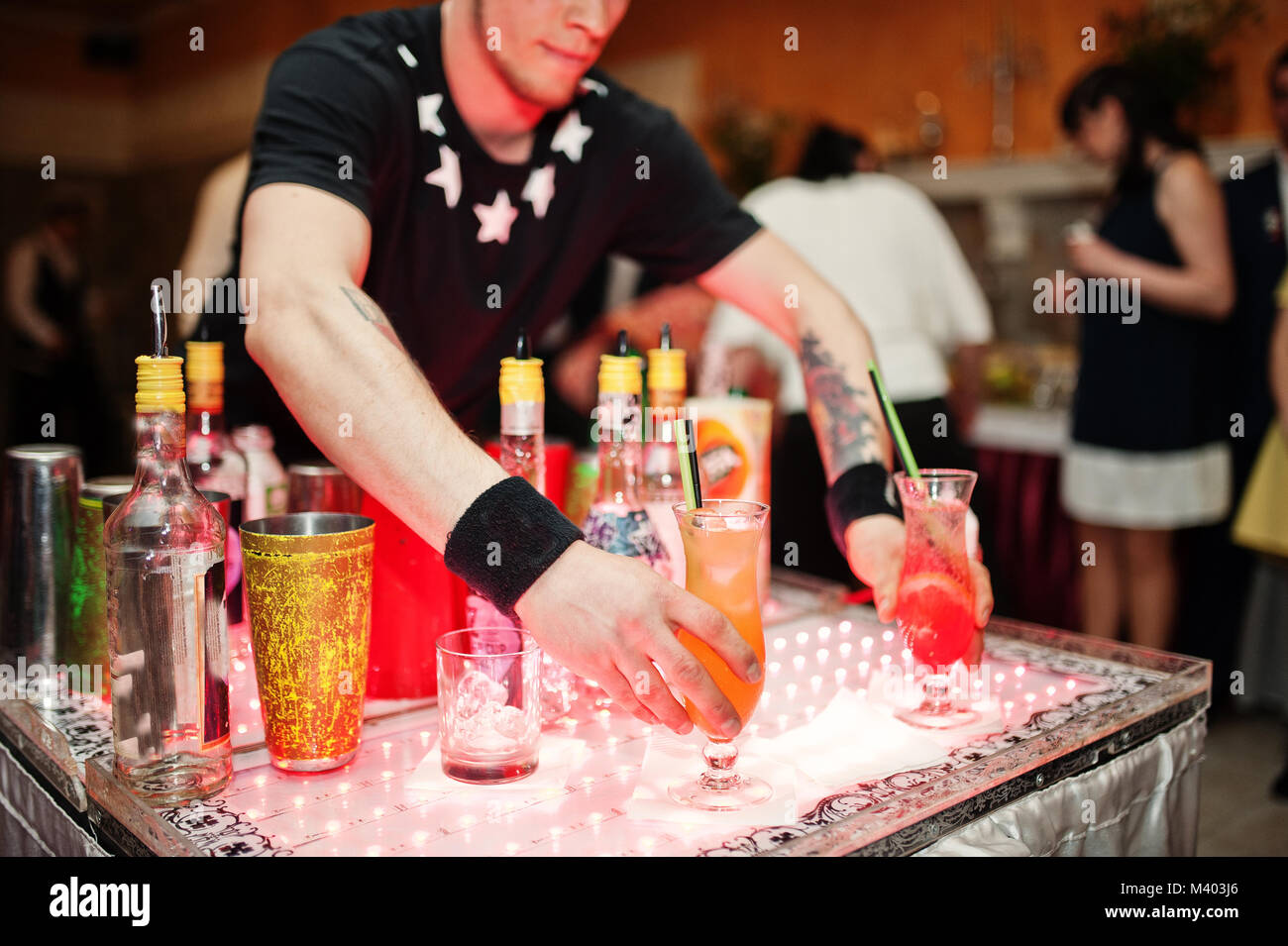 Talented bartender performing tricks with bottles and glasses in front of guests on wedding ...