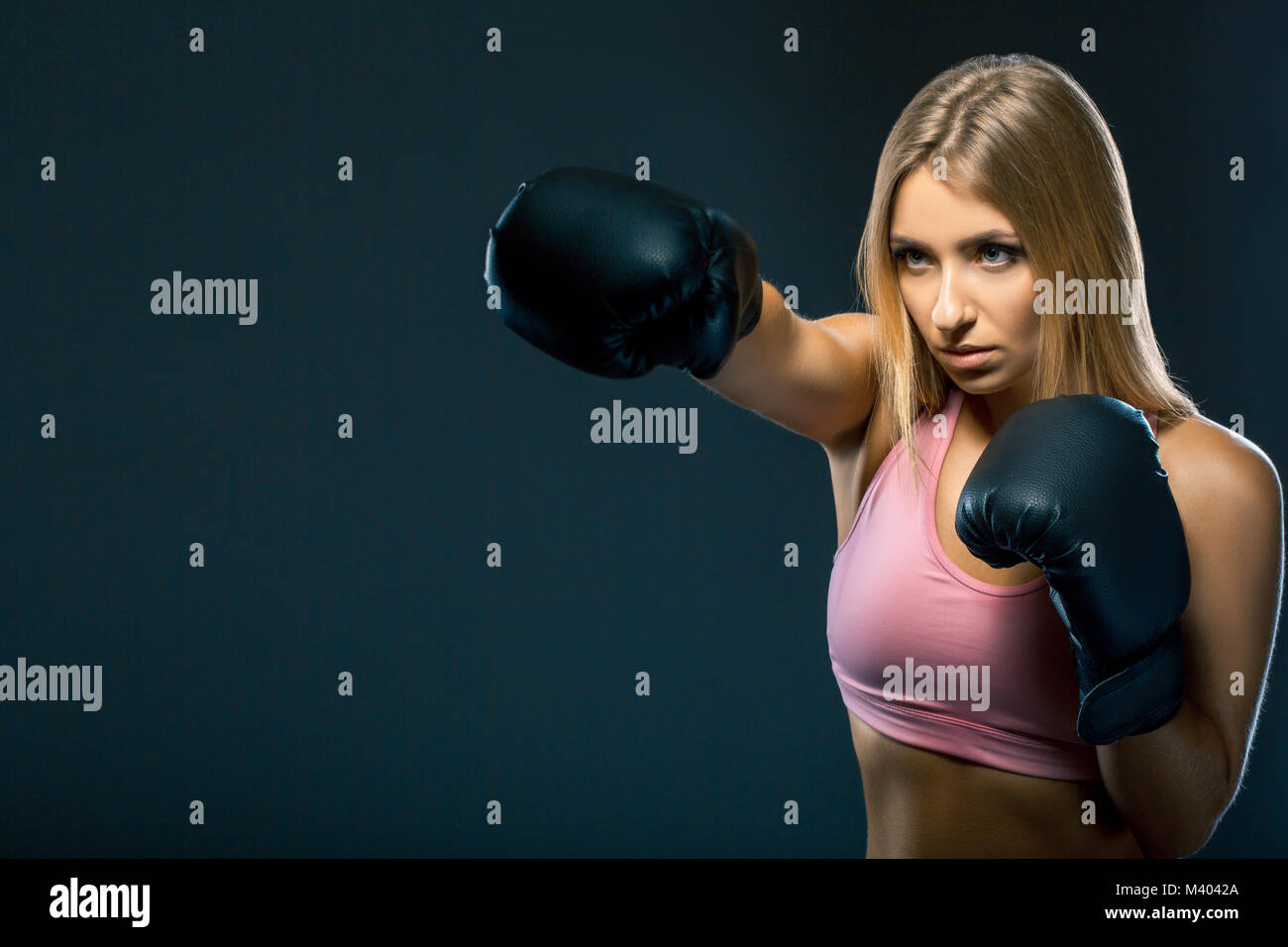 Woman in black boxing gloves and sportswear strikes at workout on dark ...