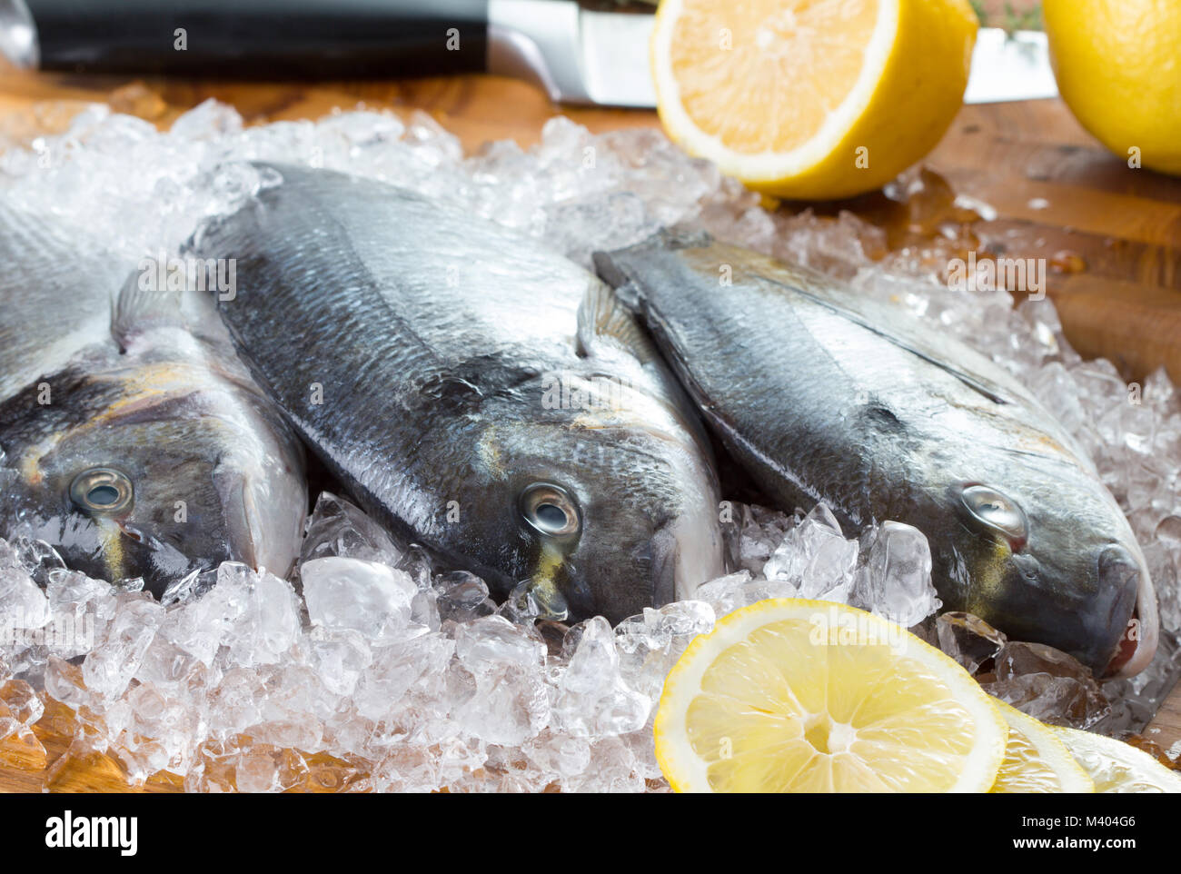three gilt-head fish and lemonon with ice on wooden plate Stock Photo ...