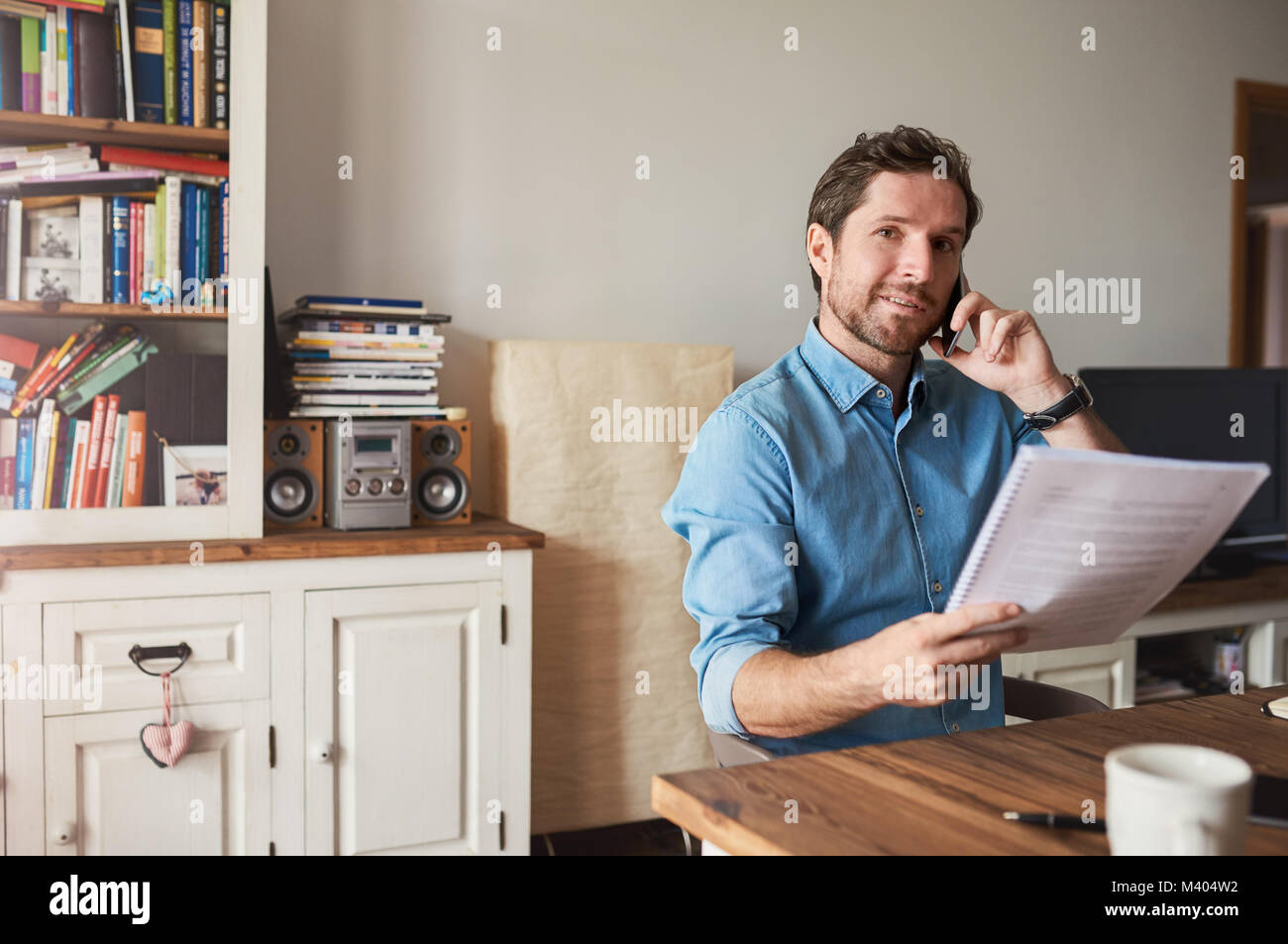 Man reading documents and talking on a cellphone at home Stock Photo ...