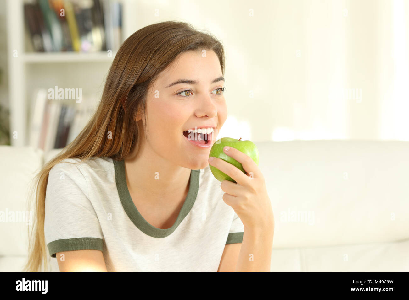 Happy teen eating an apple sitting on a couch in the living room at ...