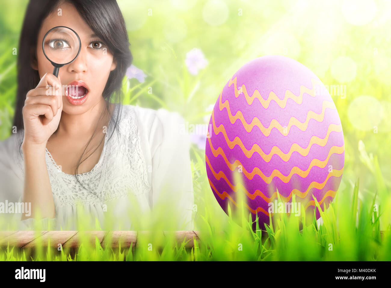 Young asian woman with magnifier finding easter egg on green grass ...