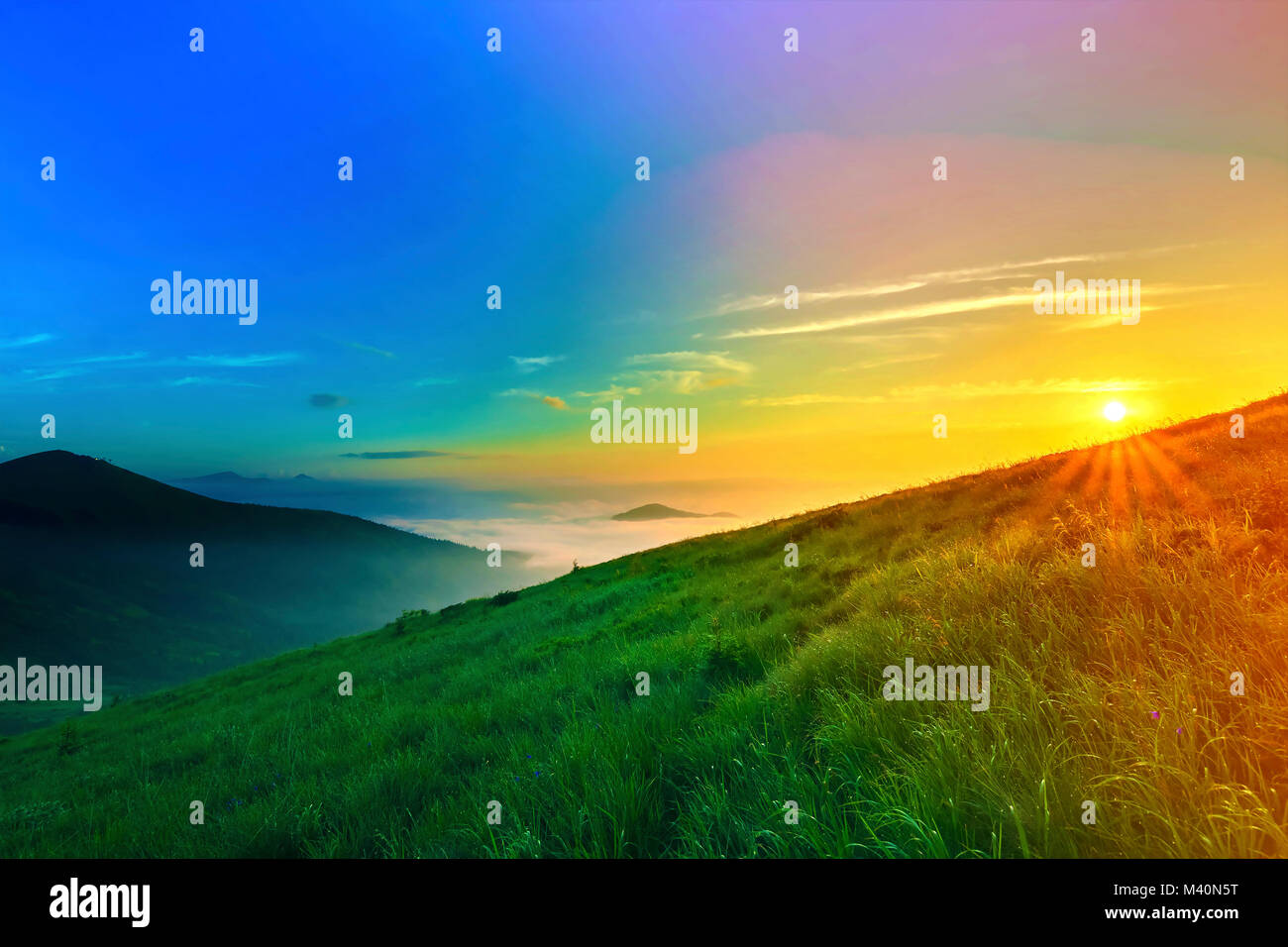 Sunrise over hills in mountains with green grass and blue sky with ...