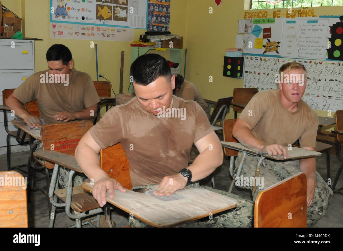 Sailors sand classroom desks to paint while doing community relations ...