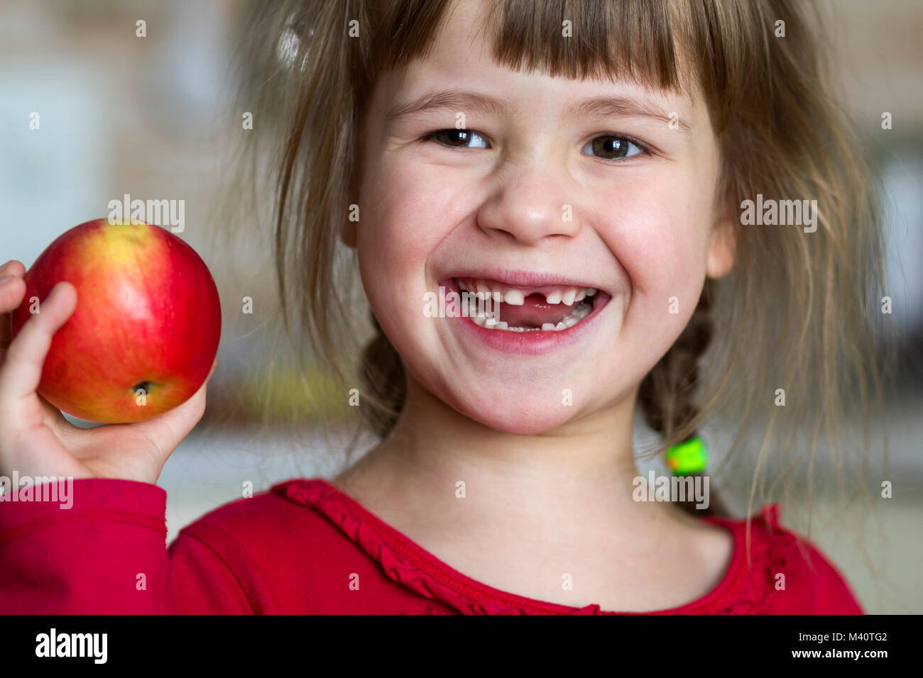 A cute little curly toothless girl smiles and holds a red apple ...