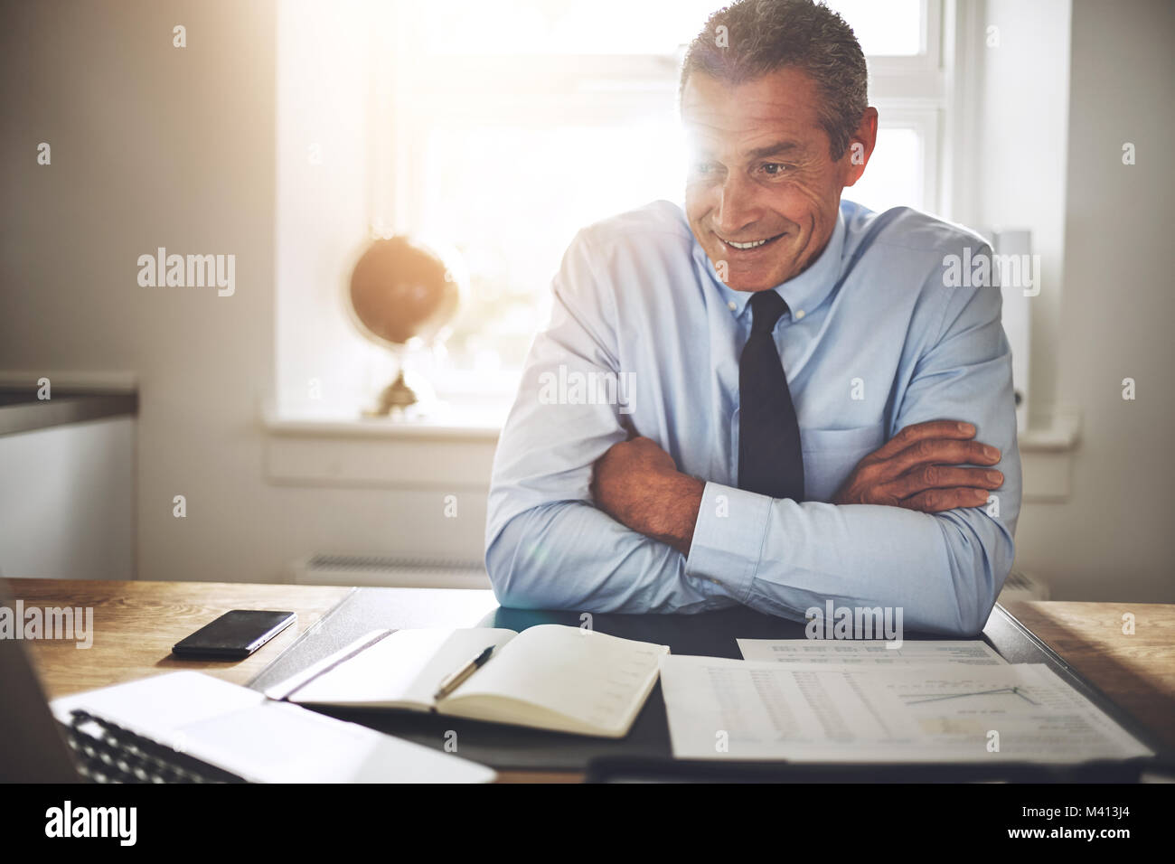 Smiling mature financial planner sitting at his desk in an office ...