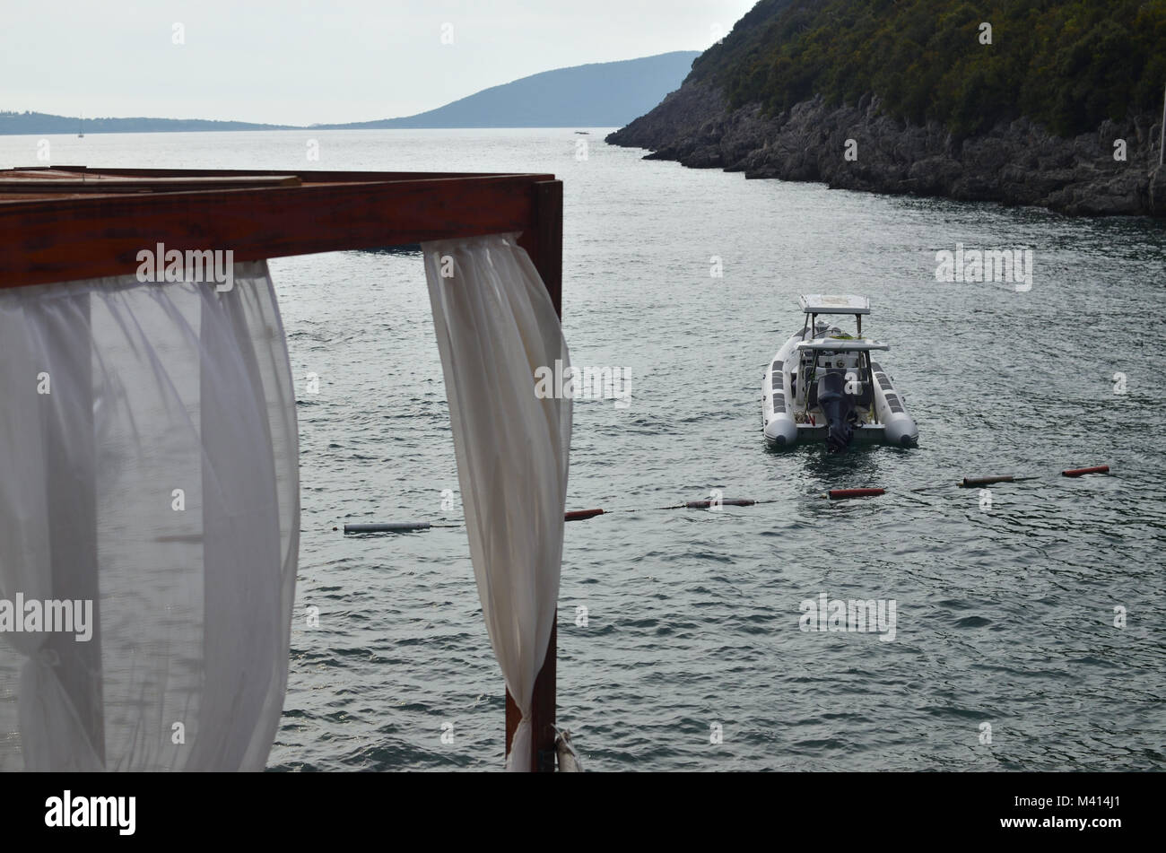 Canopy and white curtains of a cabana bed and speed boats on a calm sea ...