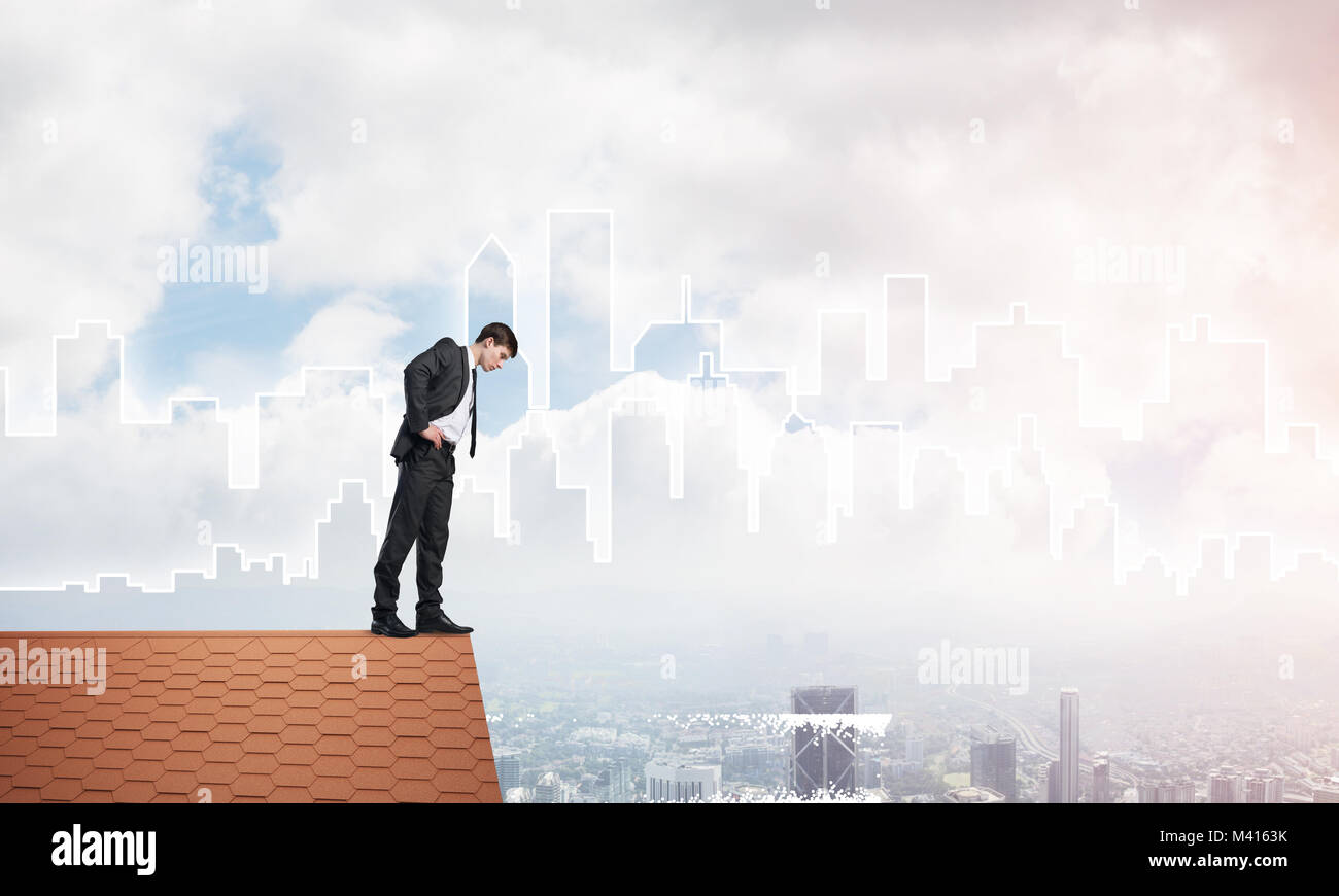 Businessman looking down from roof and modern cityscape at background ...