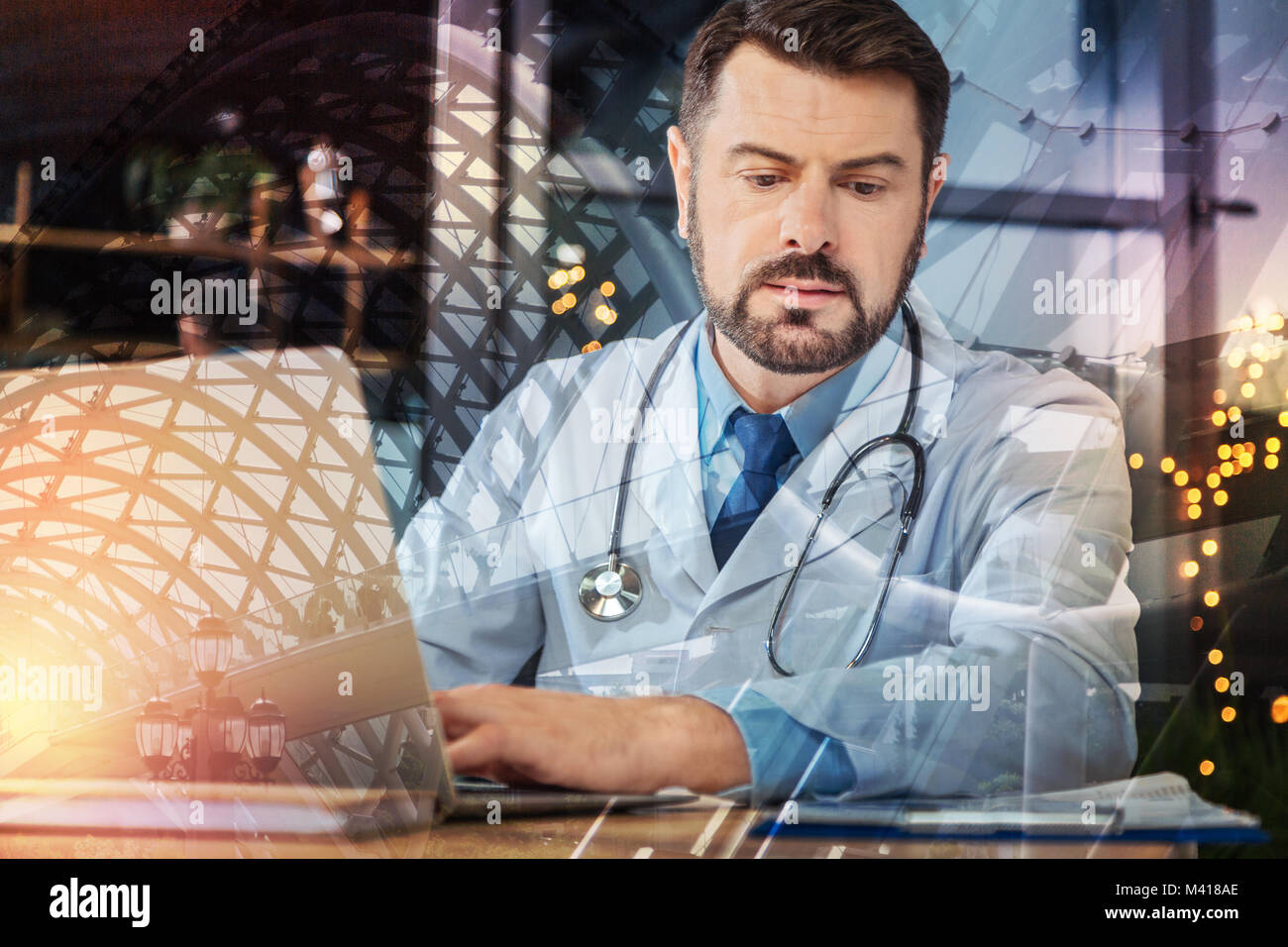 Attentive doctor typing on his laptop while looking into the notes ...