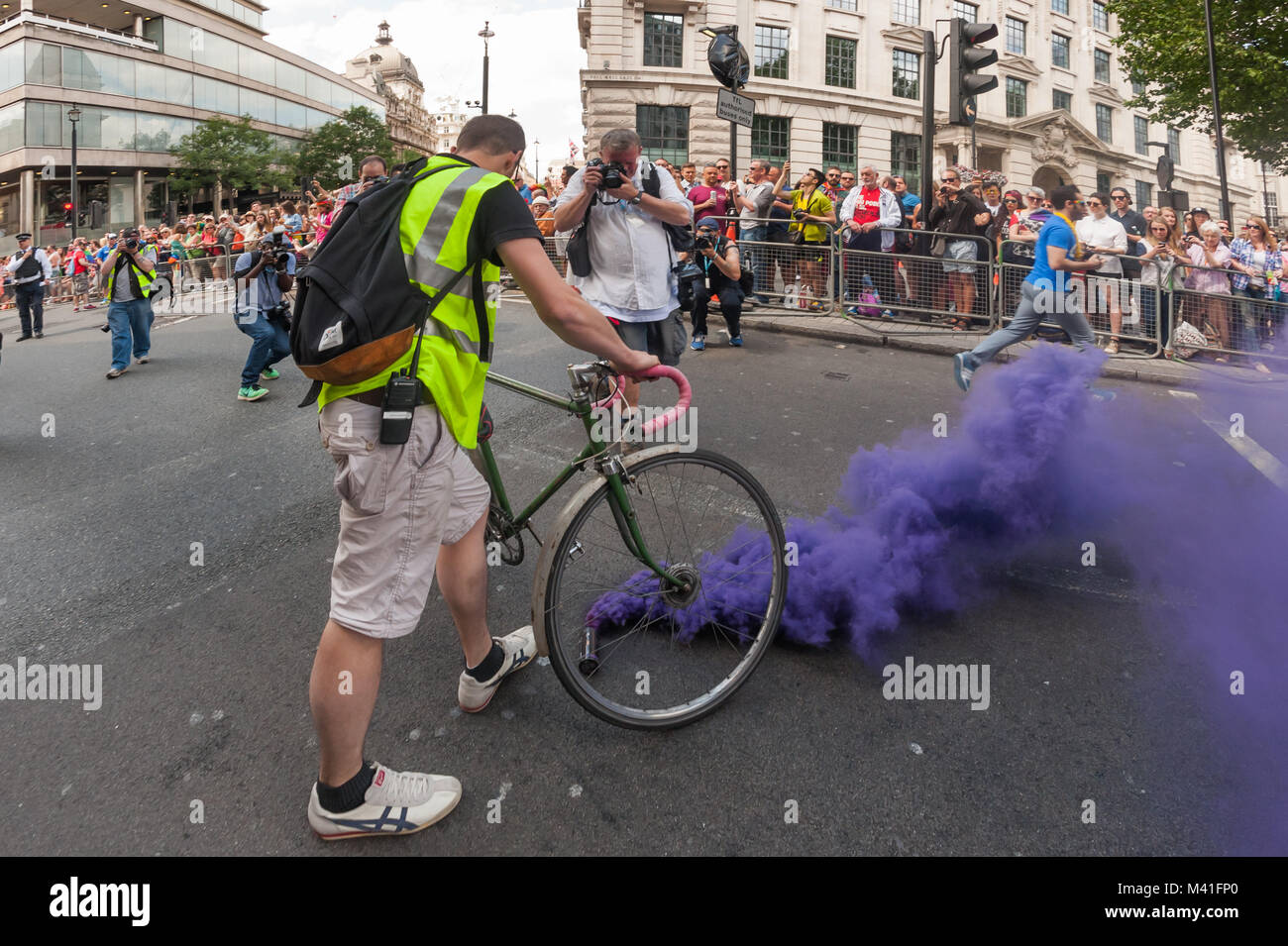 A Pride in London steward holds a bicycle and watches the mauve smoke ...