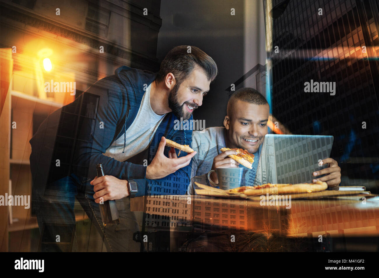 Attentive friends looking at the screen of a laptop and eating pizza ...