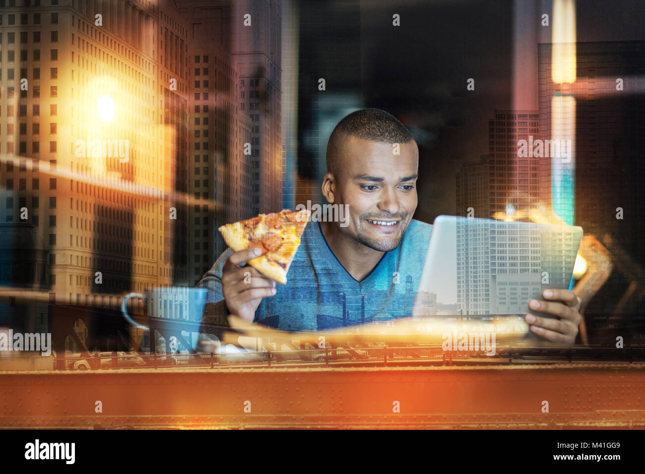 Handsome young man smiling and eating pizza while reading news Stock ...